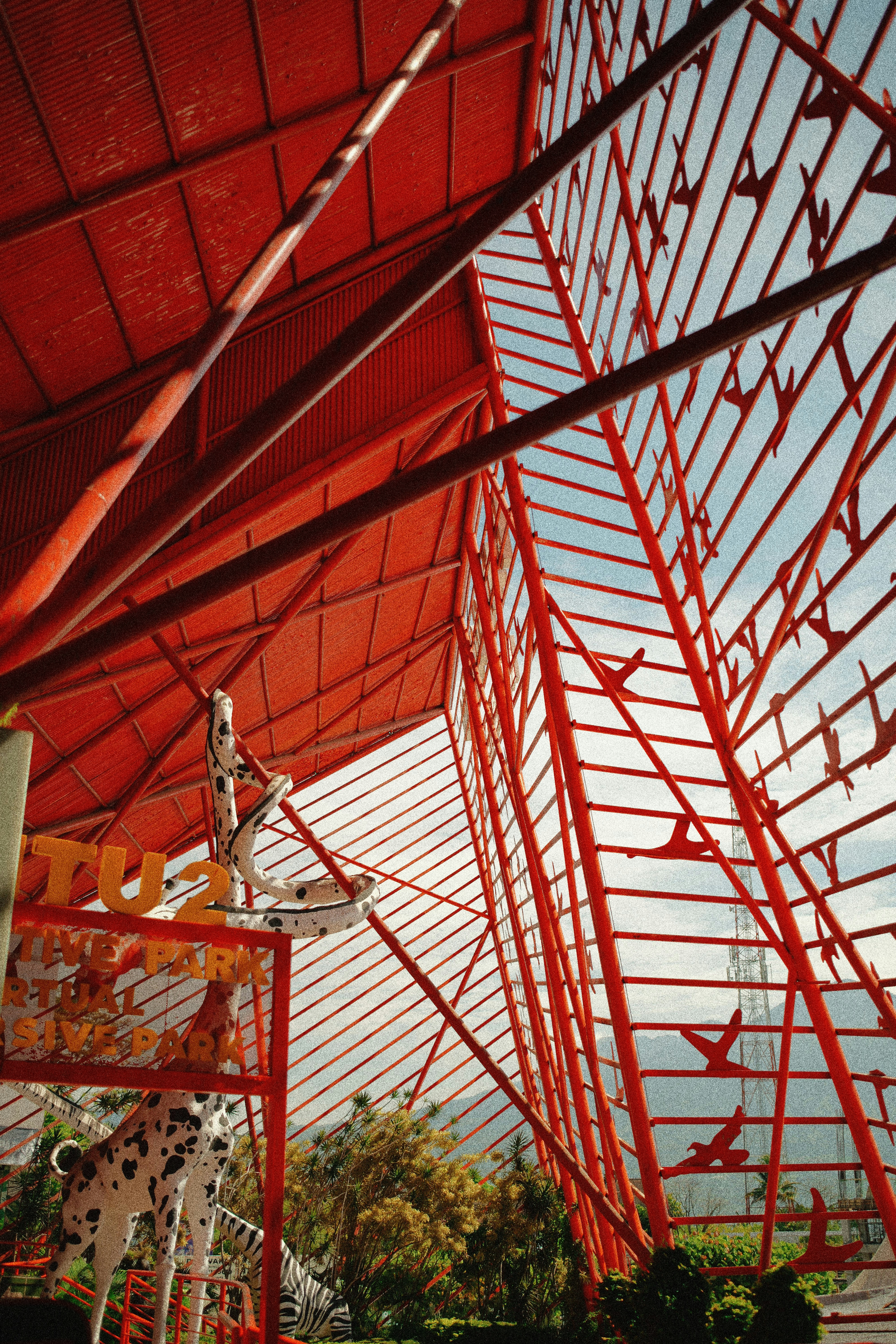 A vibrant, modern structure featuring a large, playful animal sculpture and intricate red latticework against a clear sky.