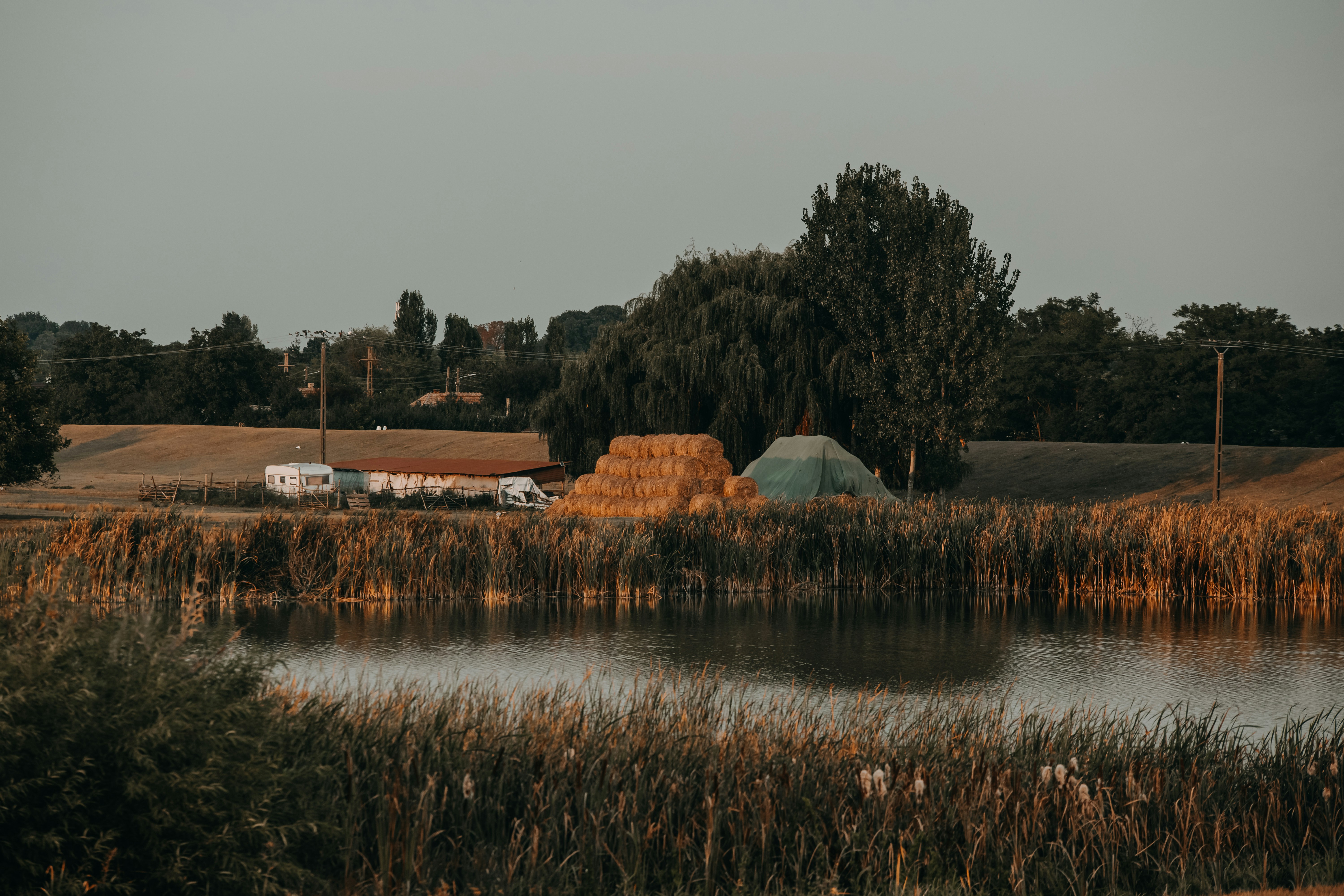 Rural landscape with a pond and hay bales at sunset