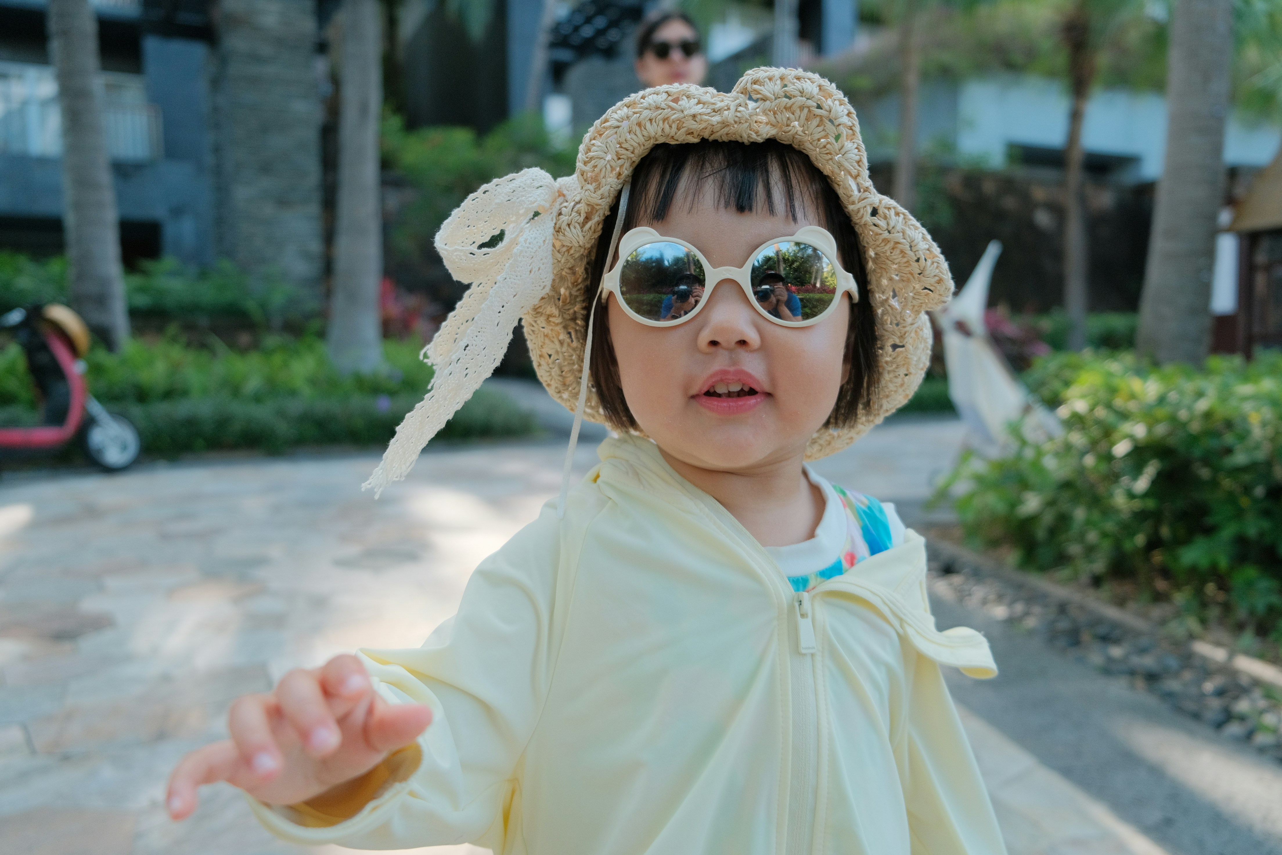 A young child wearing sunglasses and a hat outdoors.