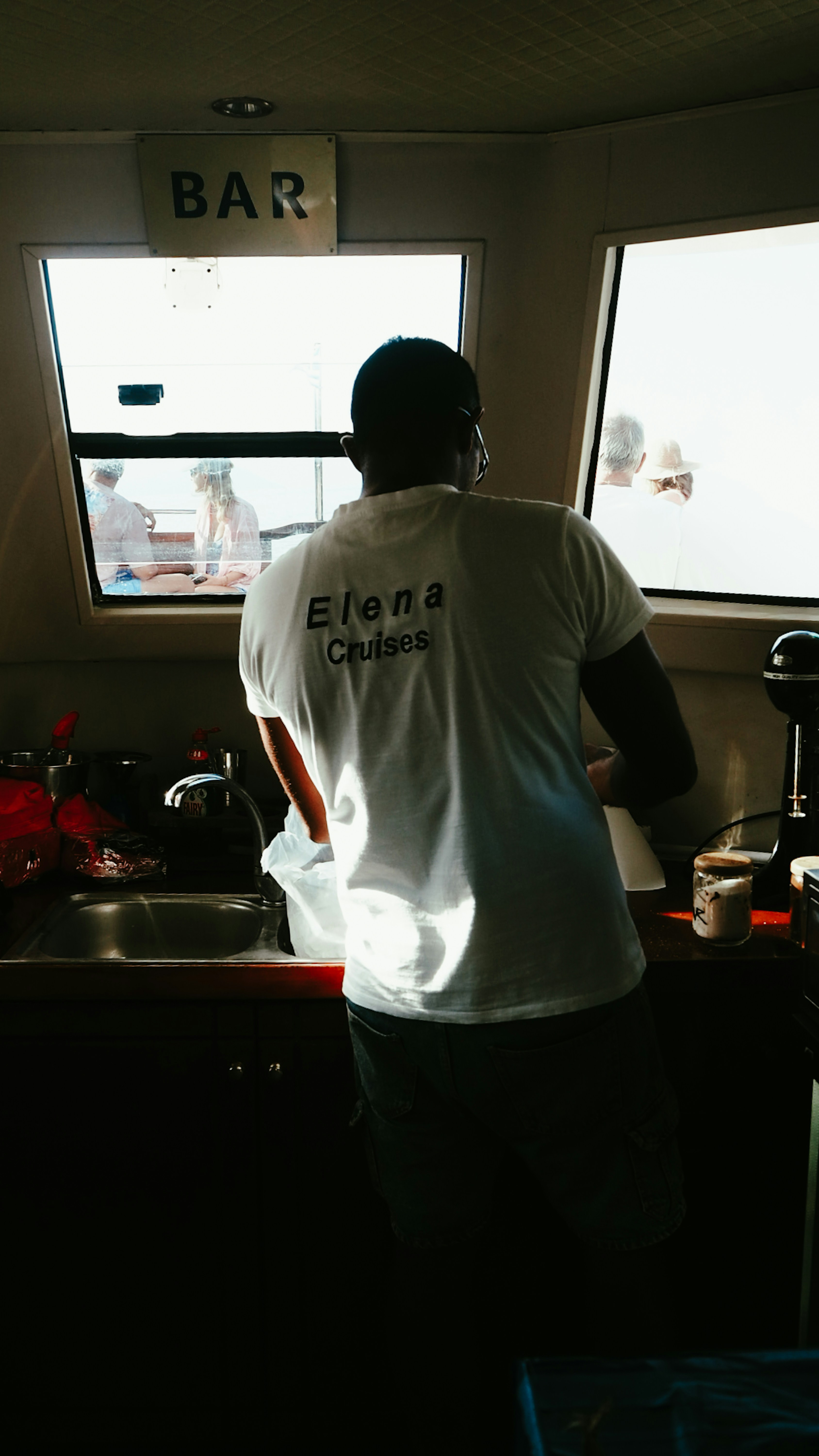 Man in "elena cruises" shirt works behind bar
