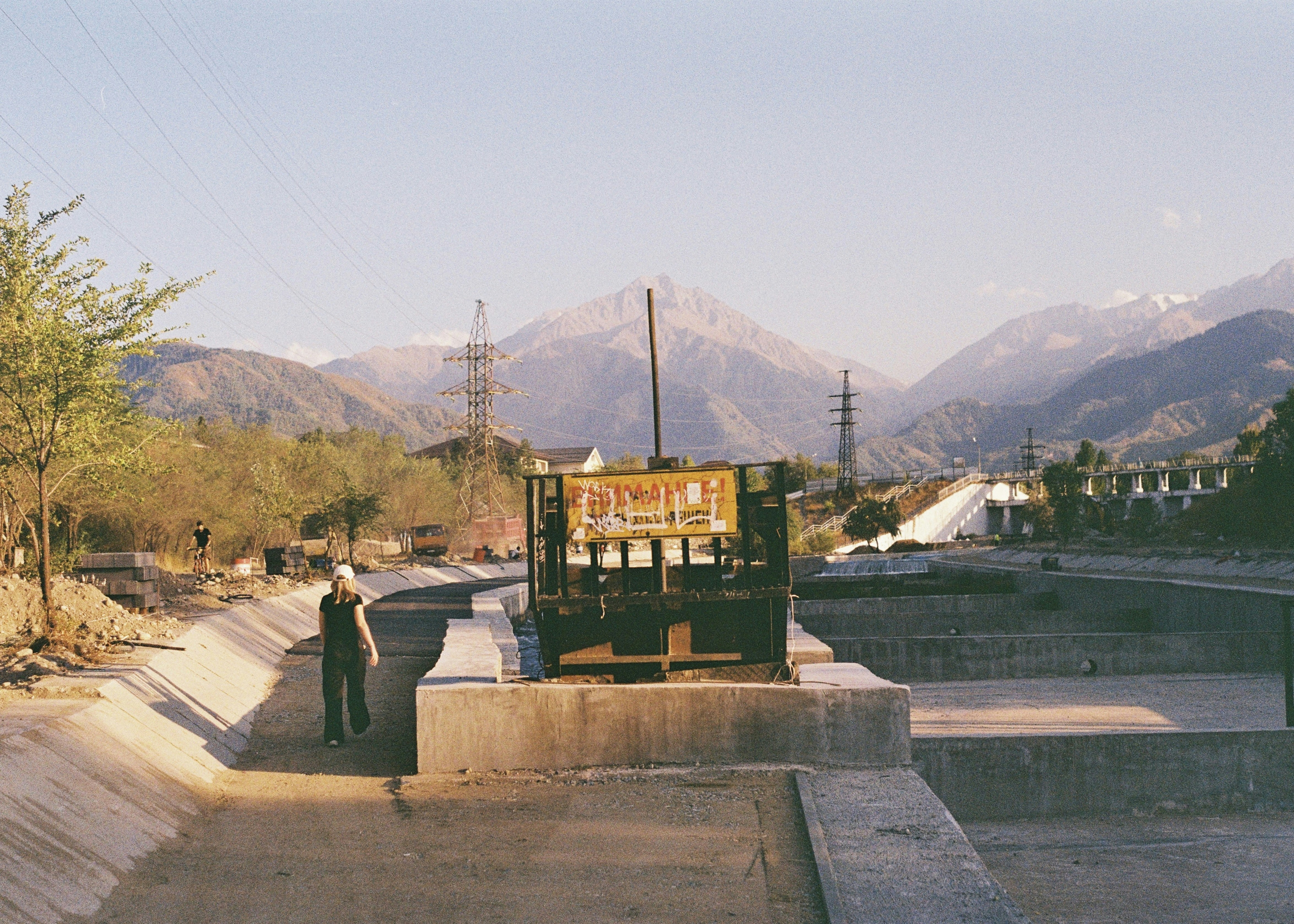 Person standing by a water channel with mountains behind