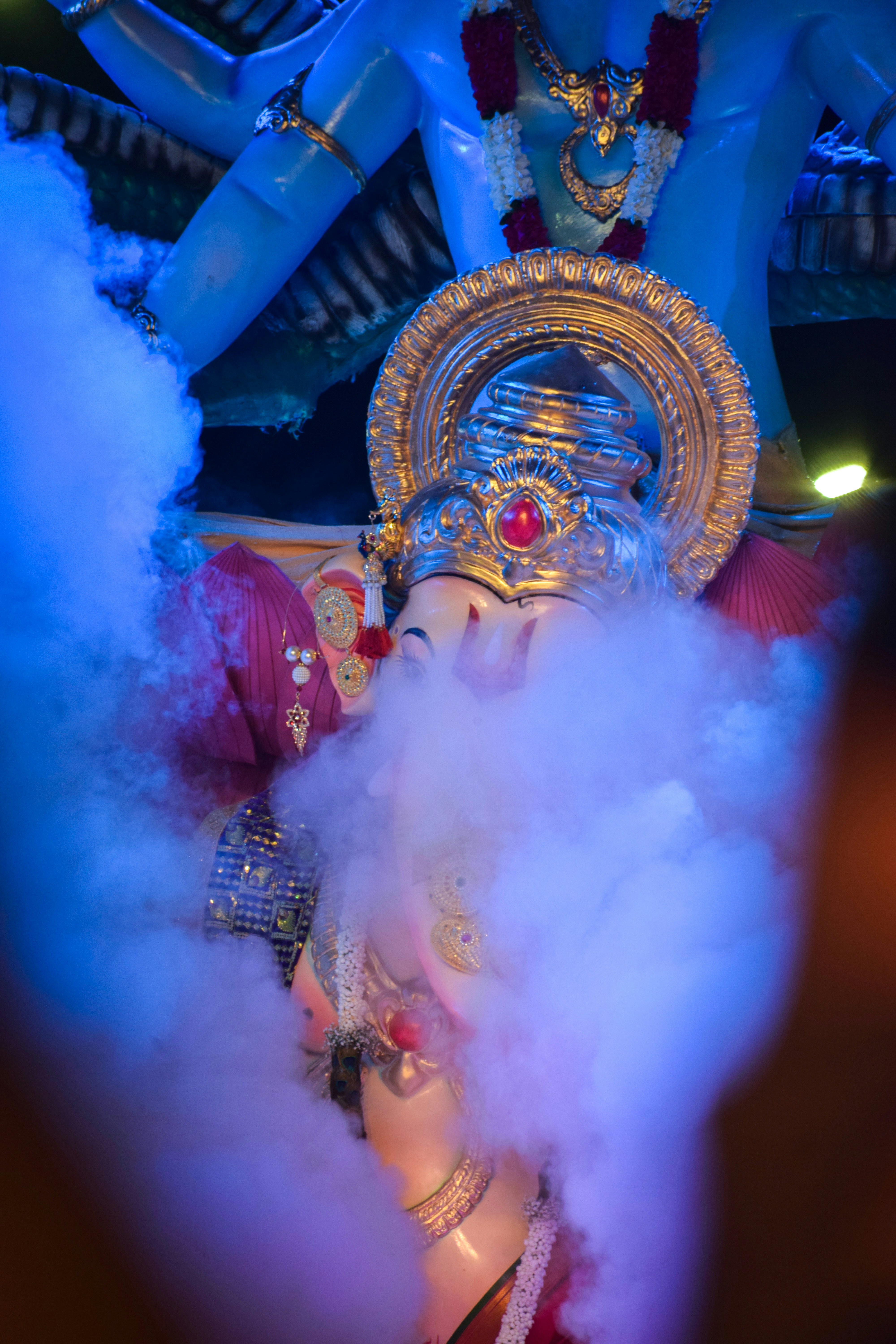 A beautifully adorned idol of Lord Ganesh partially obscured by swirling smoke, creating a mystical atmosphere during a festive celebration.