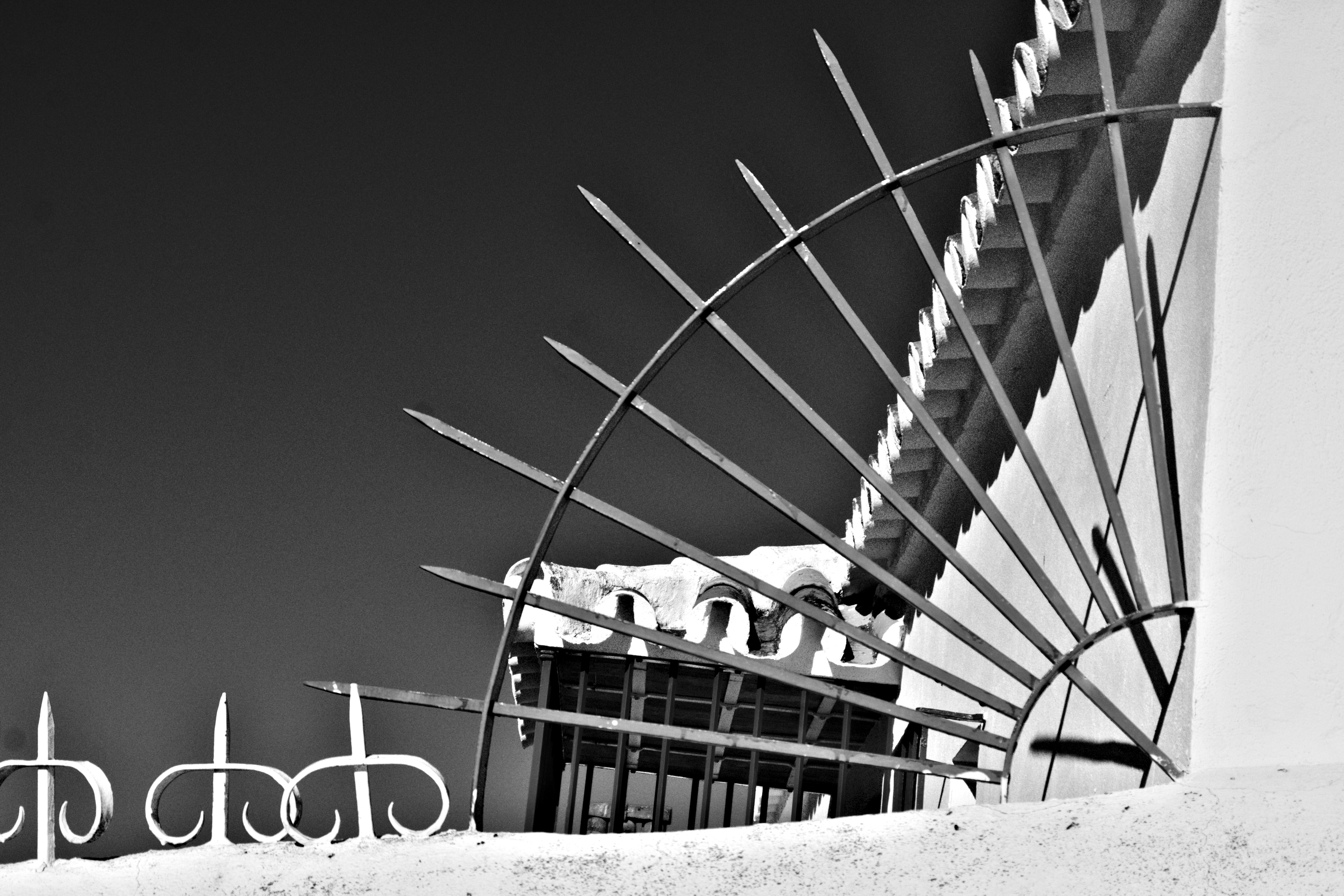 These are precautions to avoid thieves ans ronbbers to go into a house. This is popular architecture in Carmona, Seville | Black and white sunburst fence with building reflection.