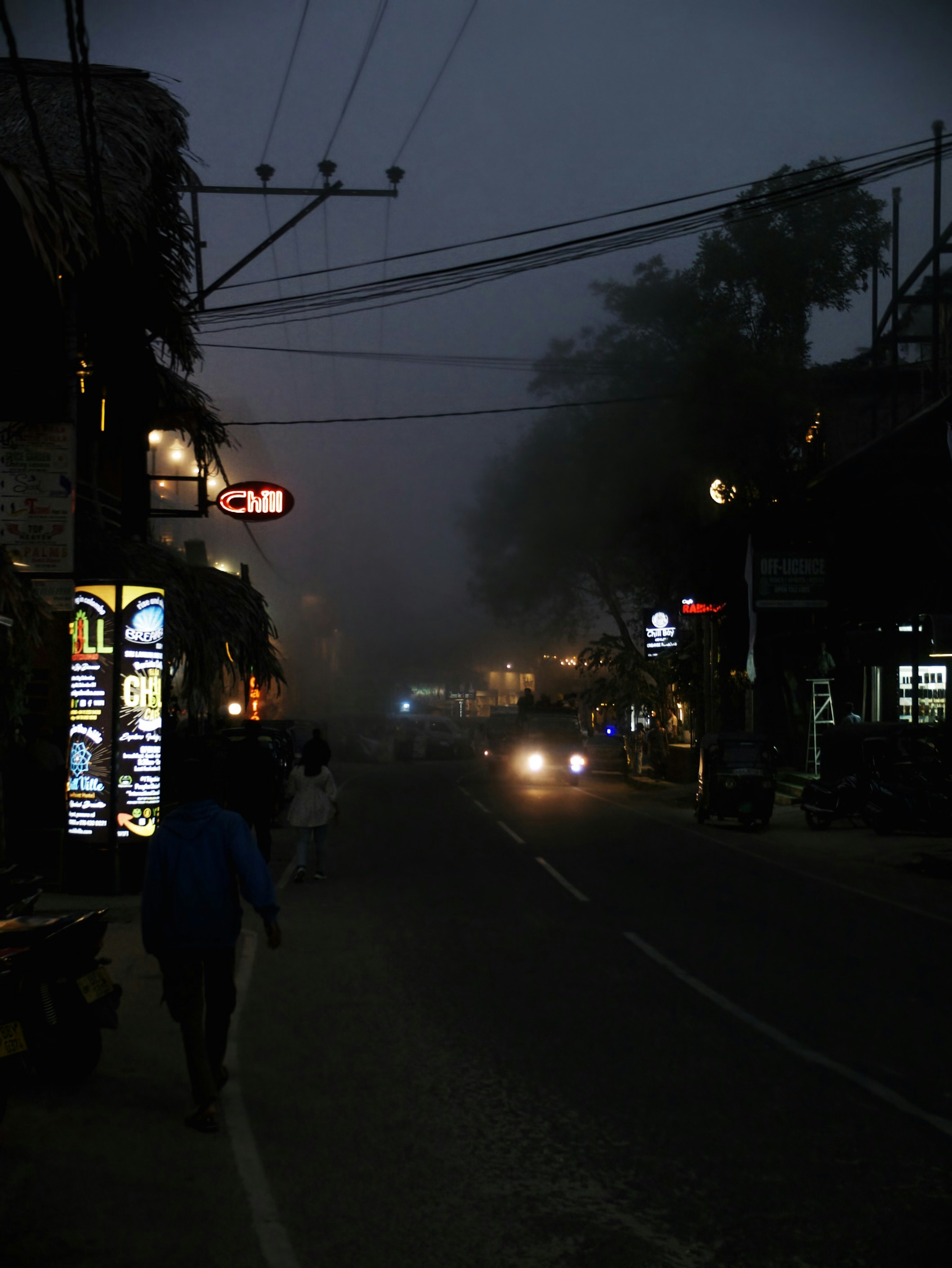 A foggy street at night with glowing signs.