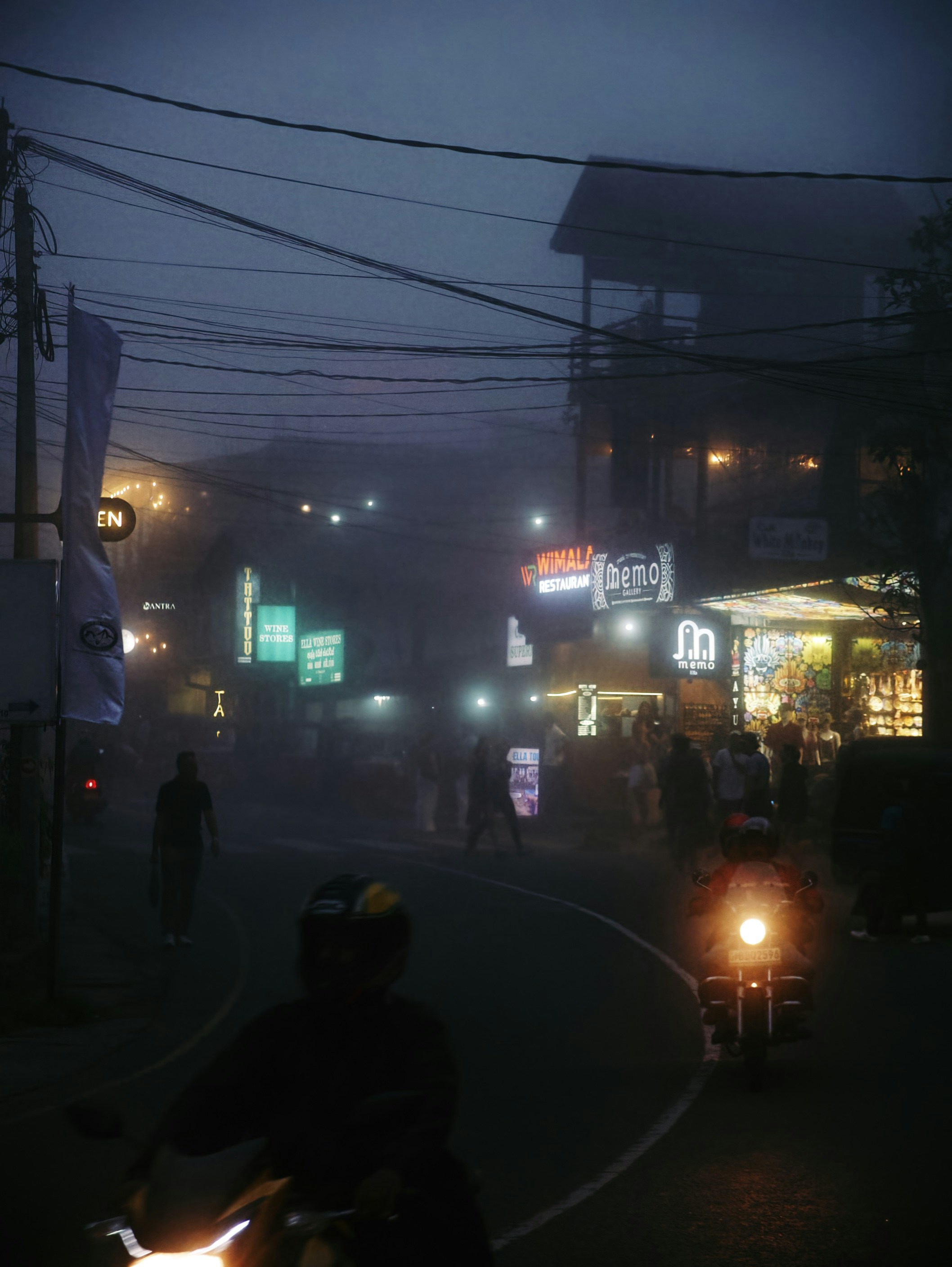 Street scene at night with neon signs and fog.