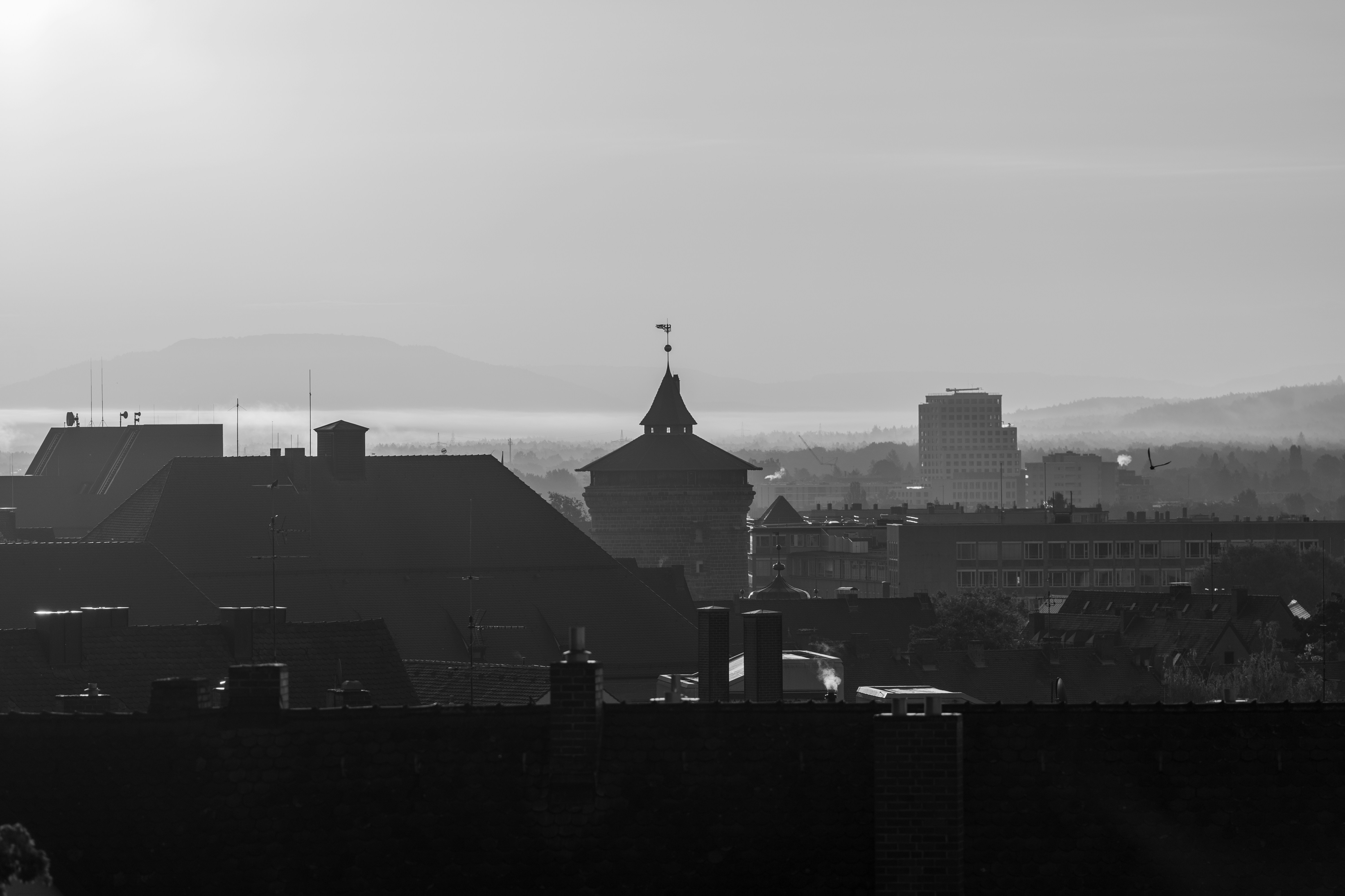 Silhouetted rooftops and a historic tower emerge from the morning mist, capturing the essence of a city steeped in history.