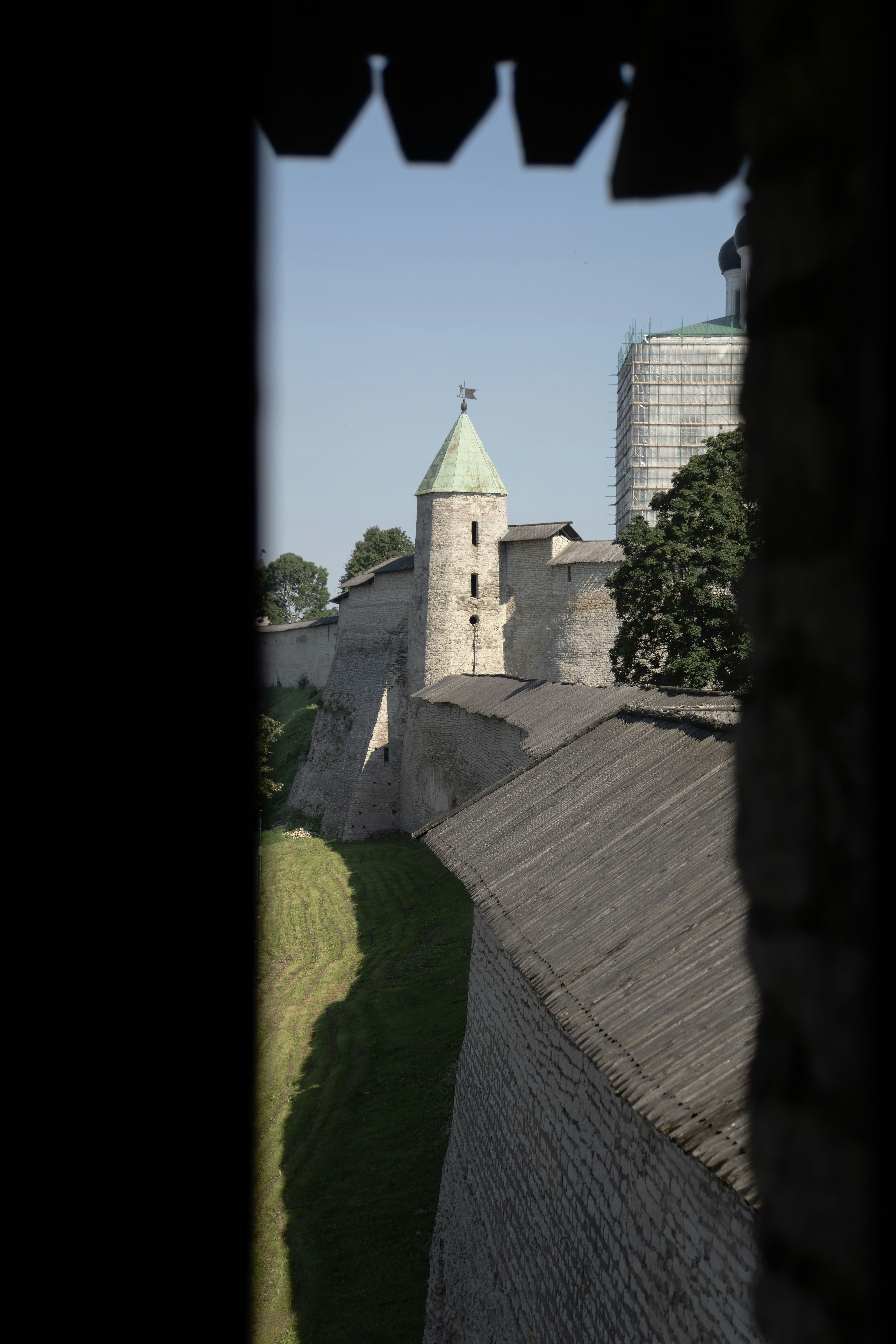 Historic stone fortress tower with a green copper roof, framed by a dark archway, showcasing a lush green landscape beyond.