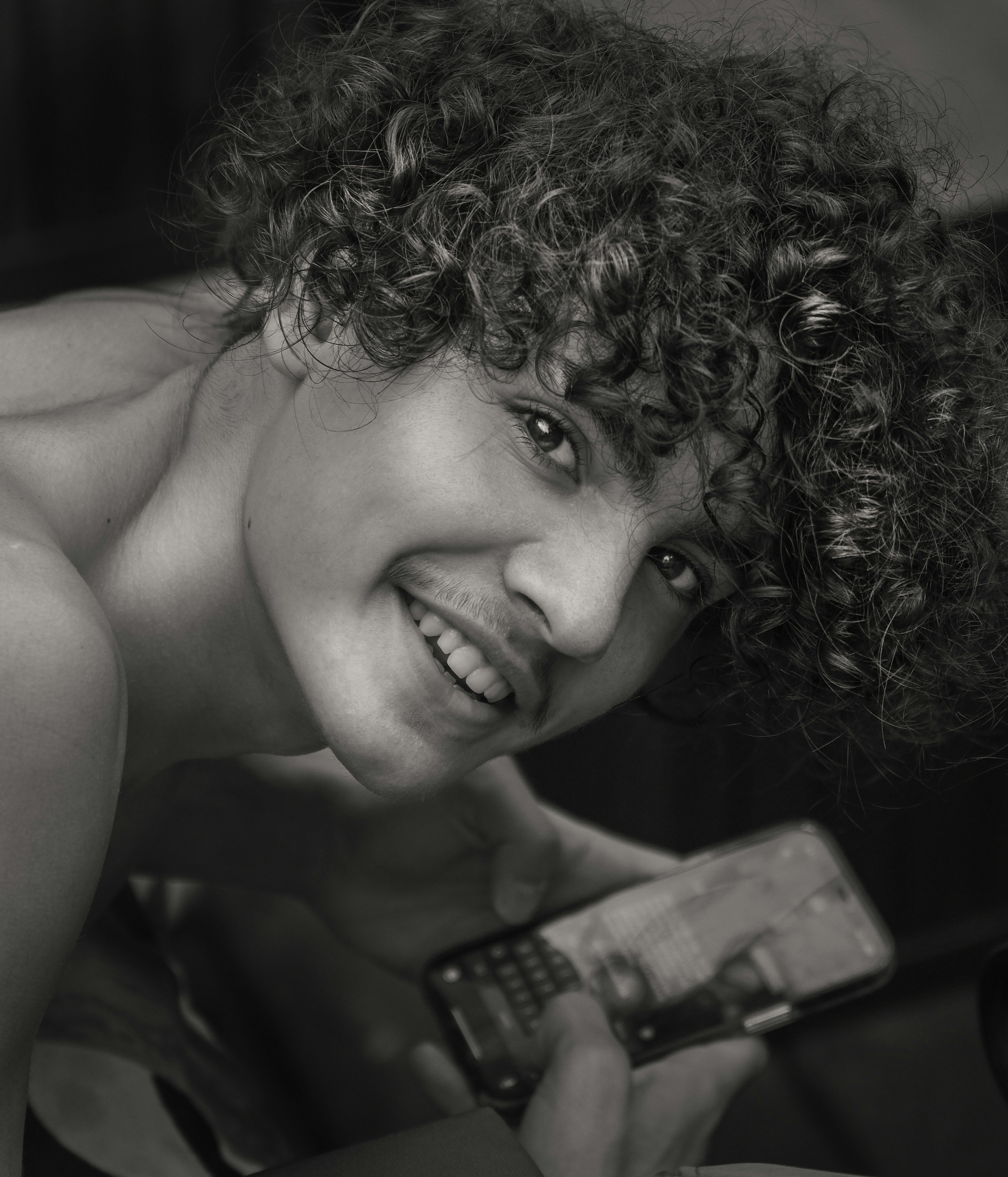 Curly Grin in Monochrome: A candid portrait framed by a handheld smartphone