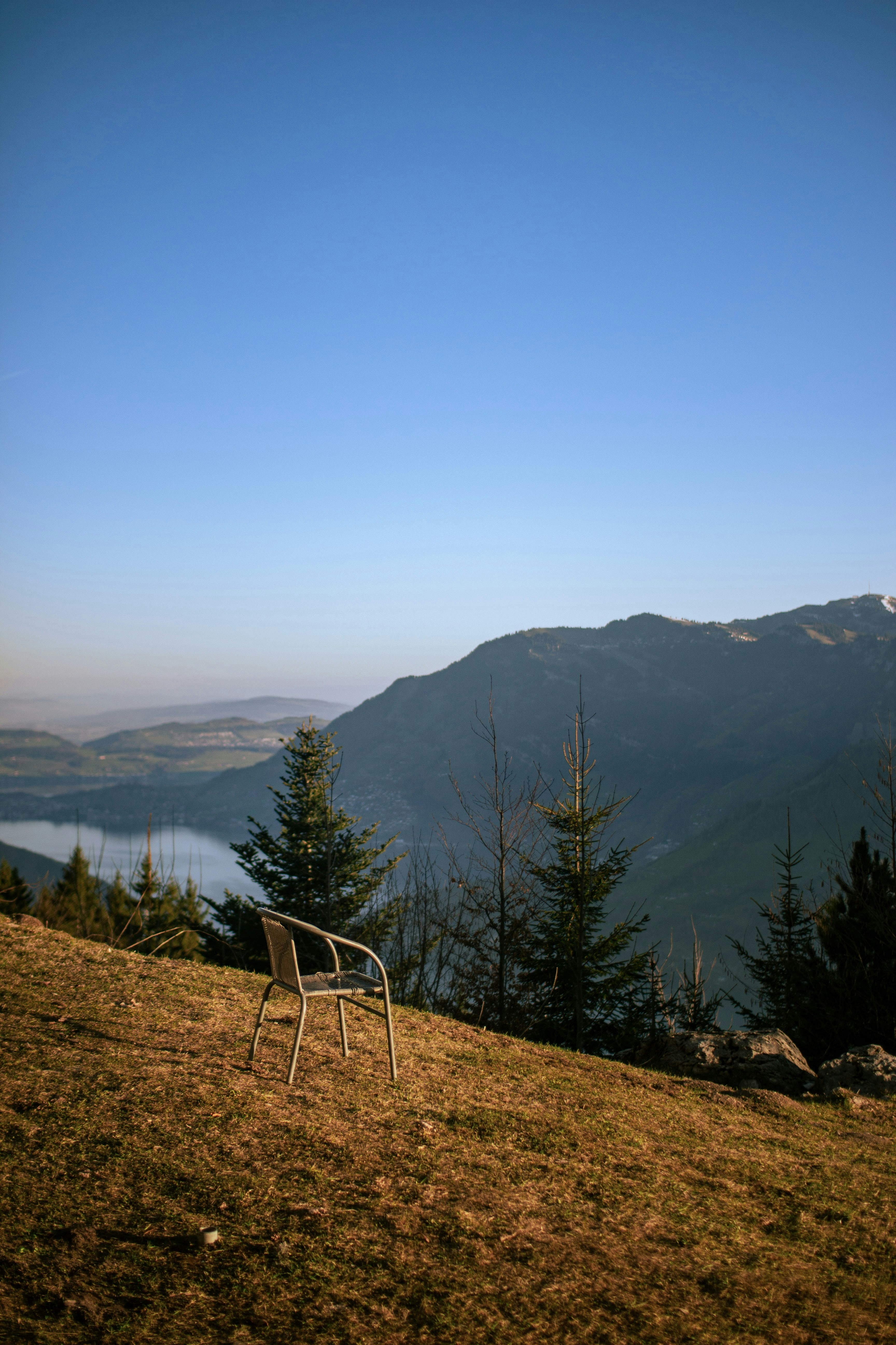 An empty chair overlooks a serene mountain lake landscape.
