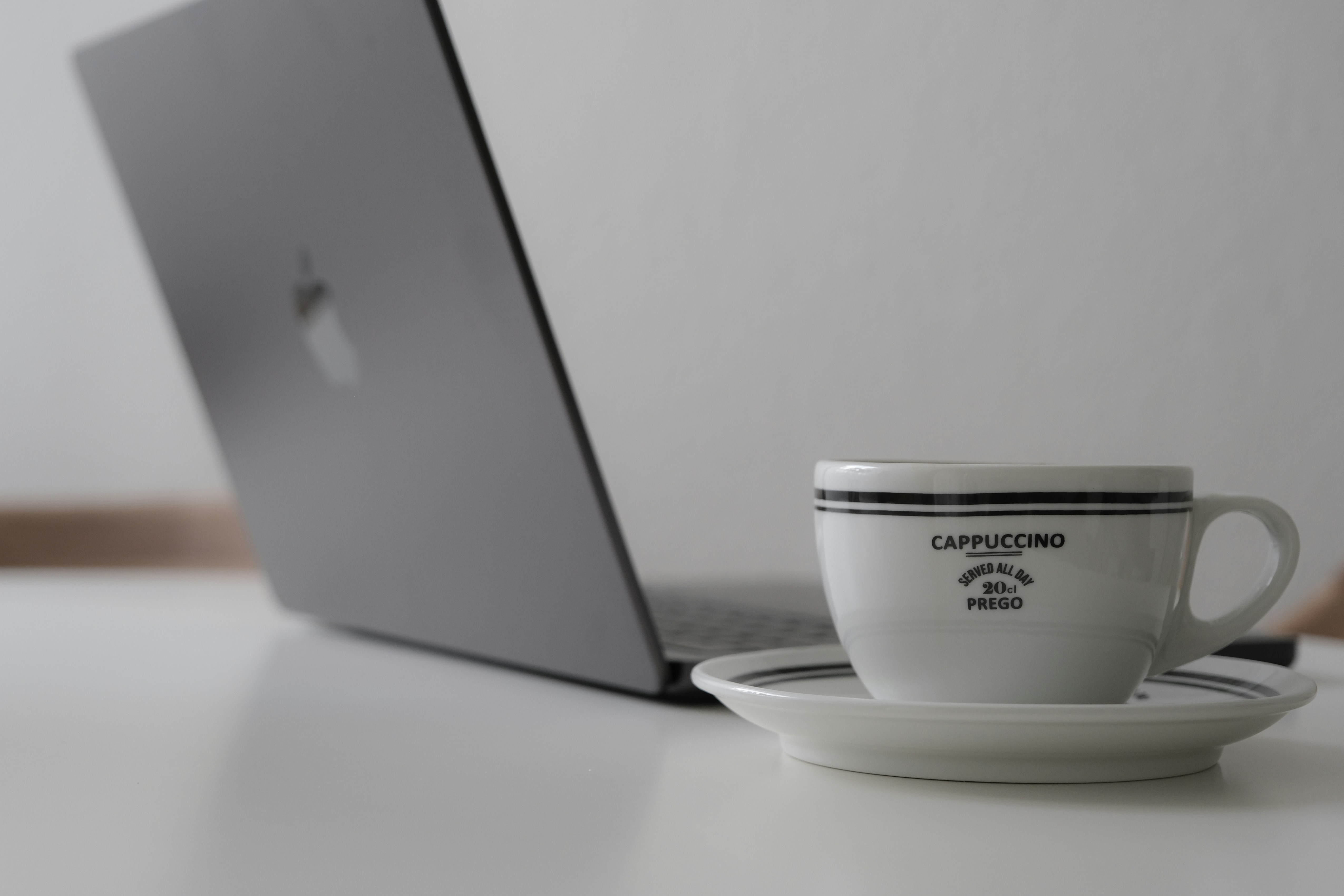A cappuccino cup on a saucer sits next to a sleek laptop, embodying a moment of tranquility in a workspace.