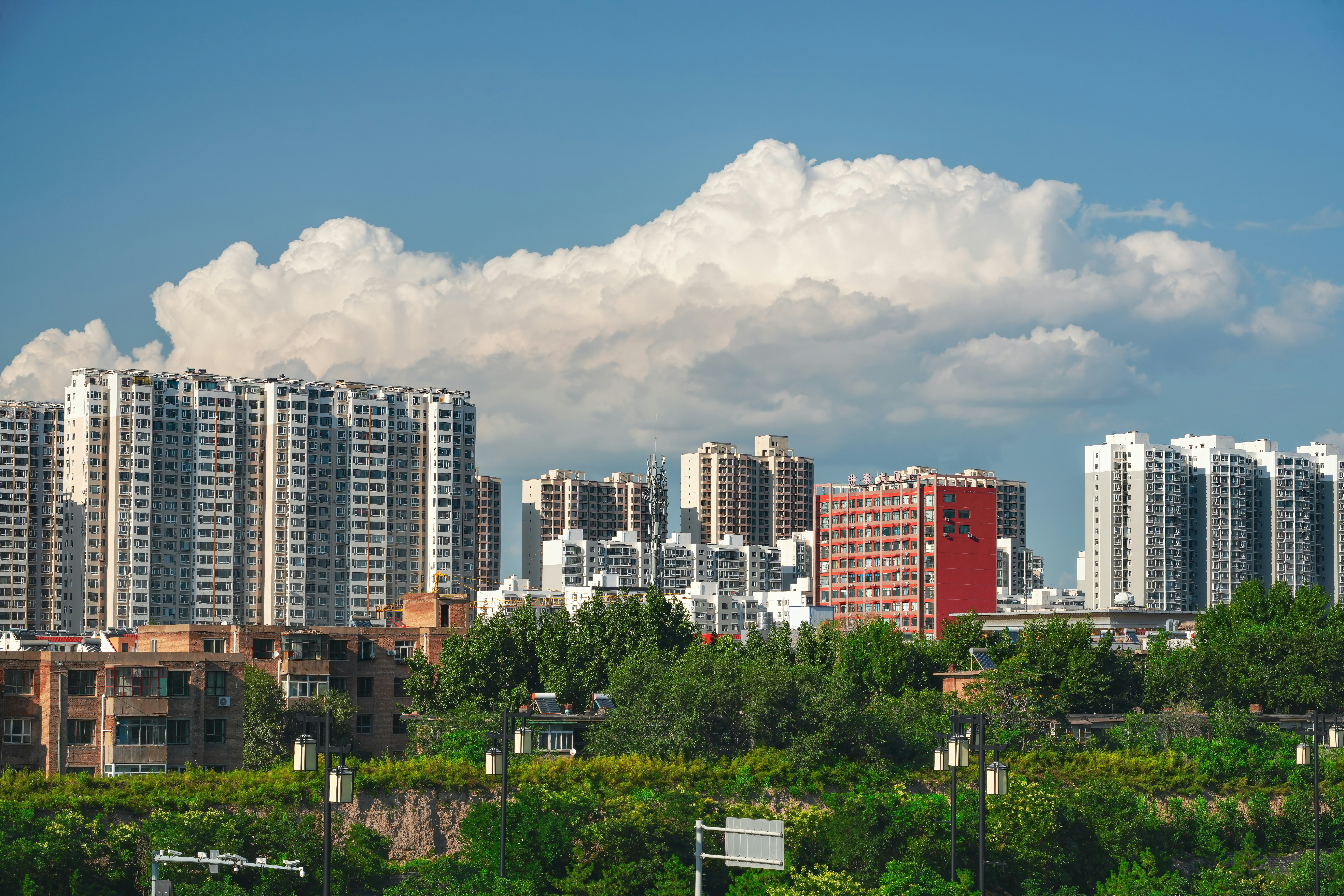 A vibrant city skyline featuring a mix of modern high-rises and greenery, with fluffy clouds overhead. The scene captures the essence of urban life intertwined with nature.