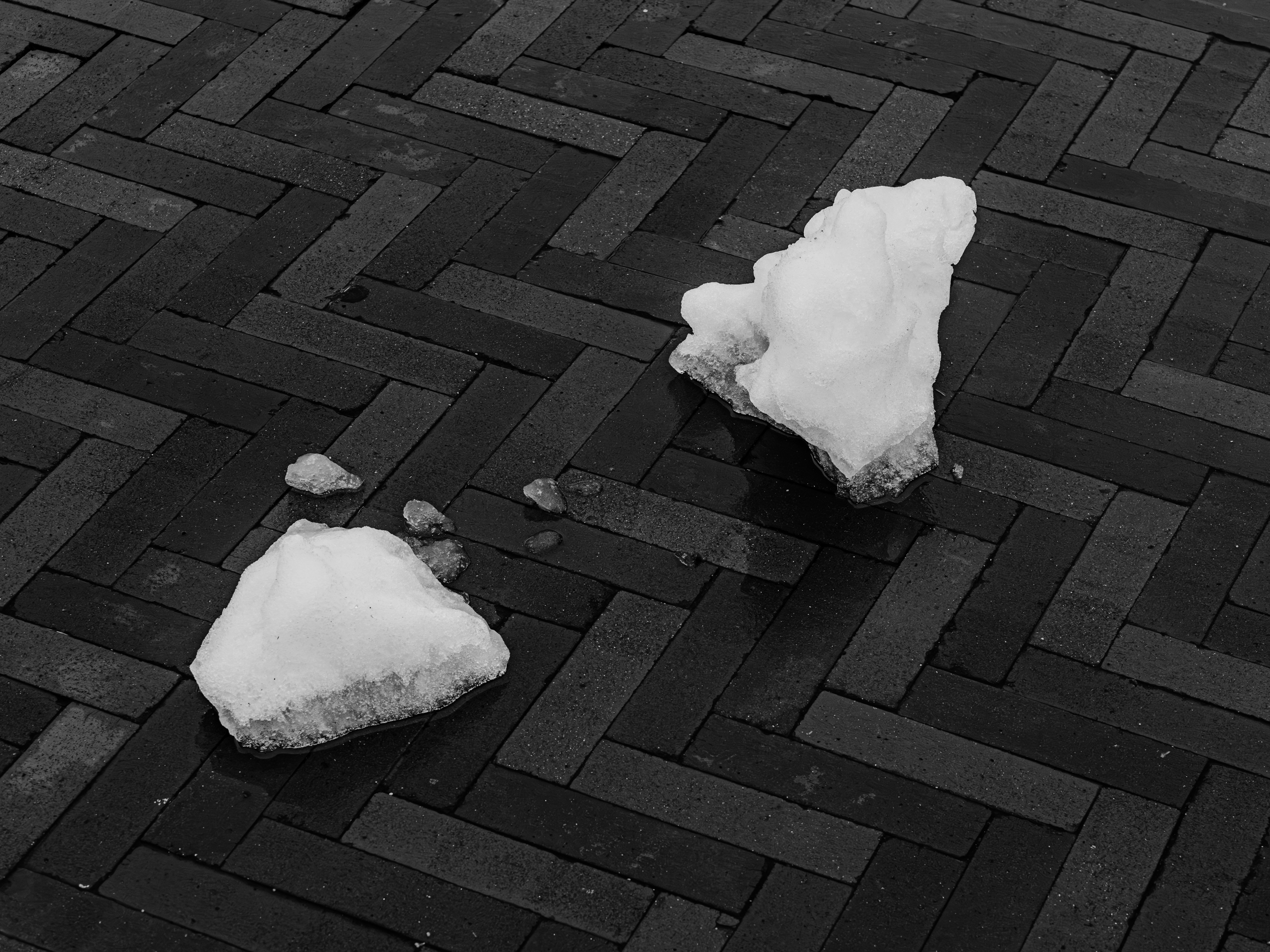 Two melting snow patches on a textured brick pavement, highlighting the transition from winter to spring.