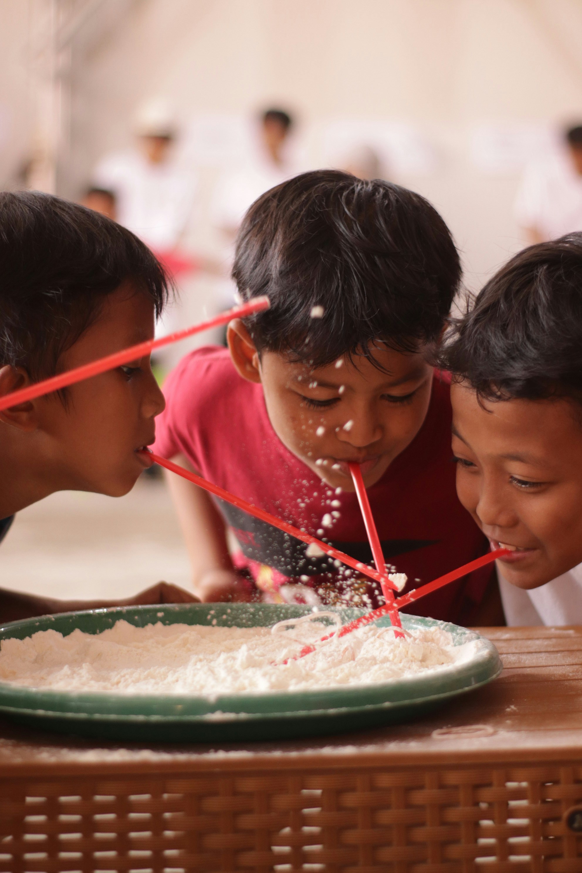 Three children compete in a playful challenge using straws to transfer flour from a plate, showcasing teamwork and fun.