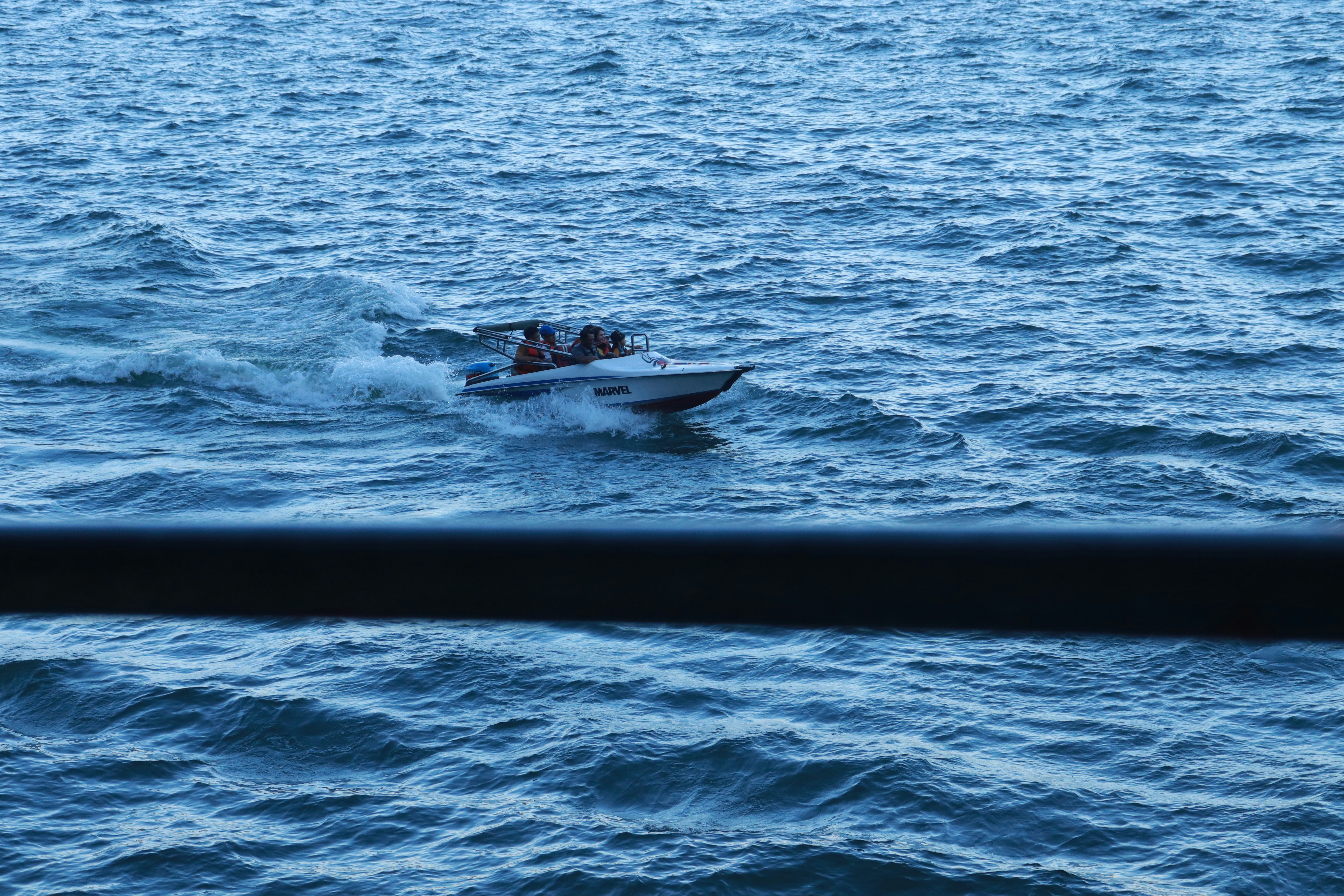 A small boat with people speeds across choppy blue water.