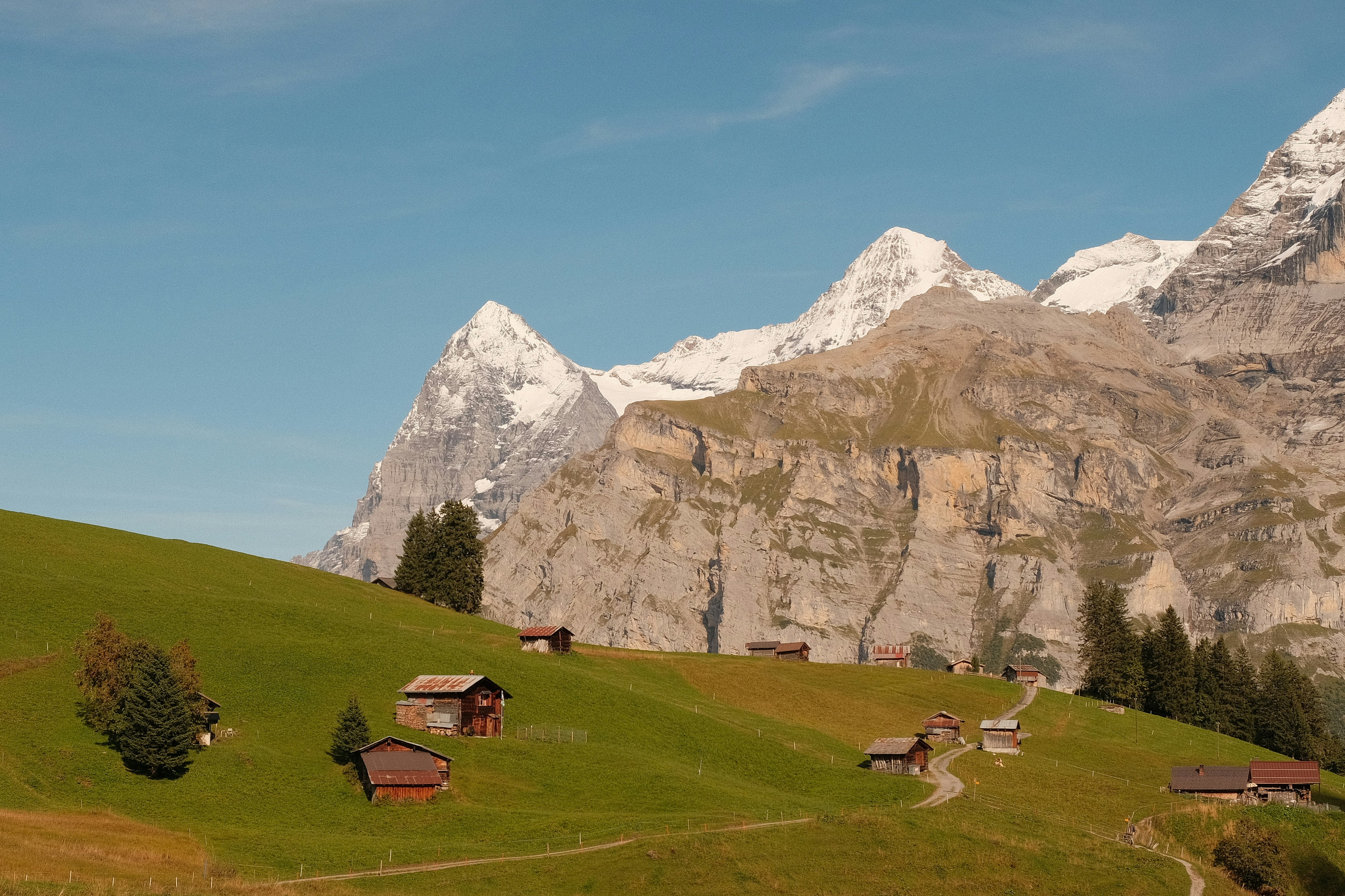Small wooden cabins on a grassy slope with mountains.