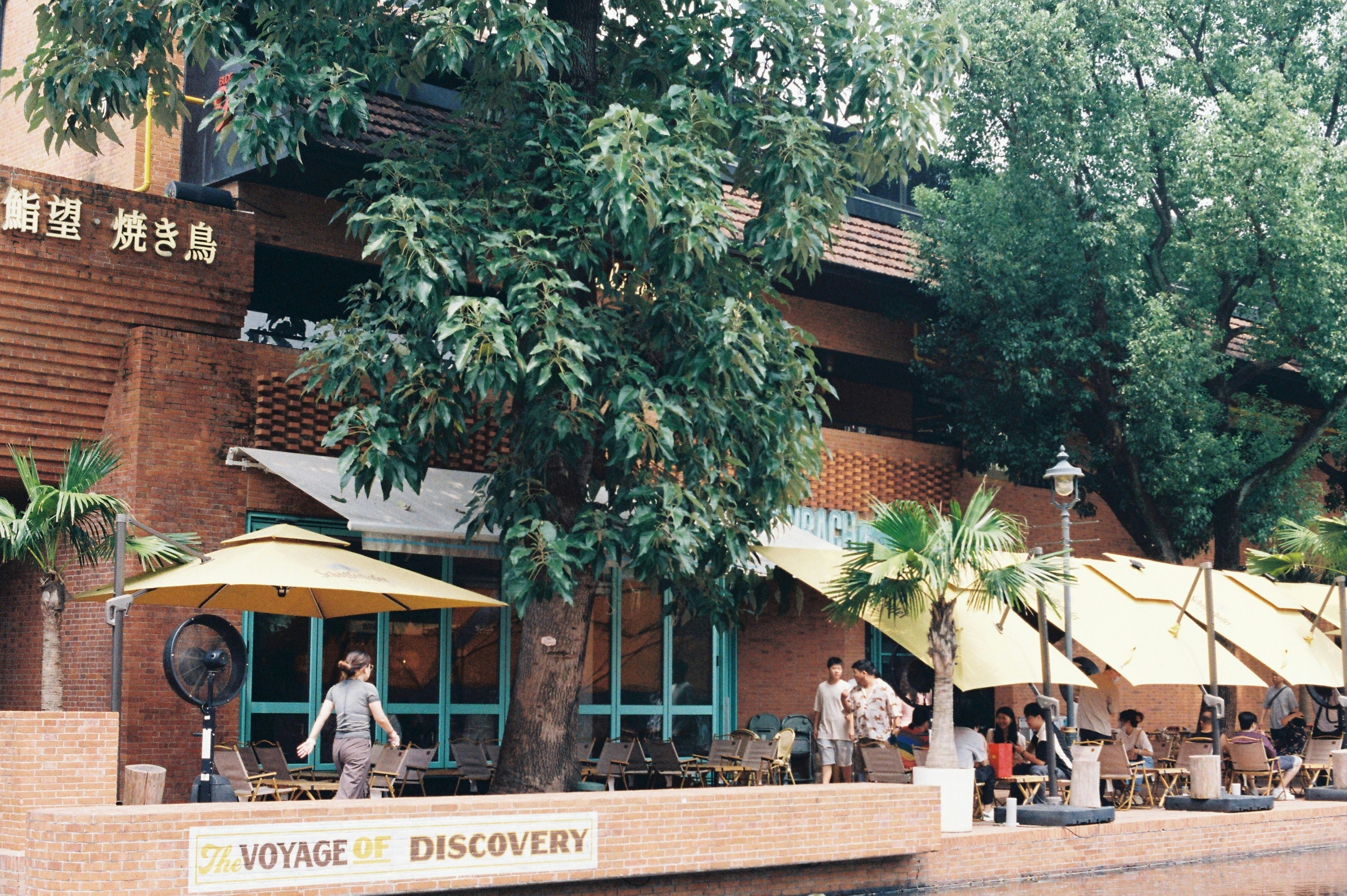 Outdoor seating area beside a brick building with trees.