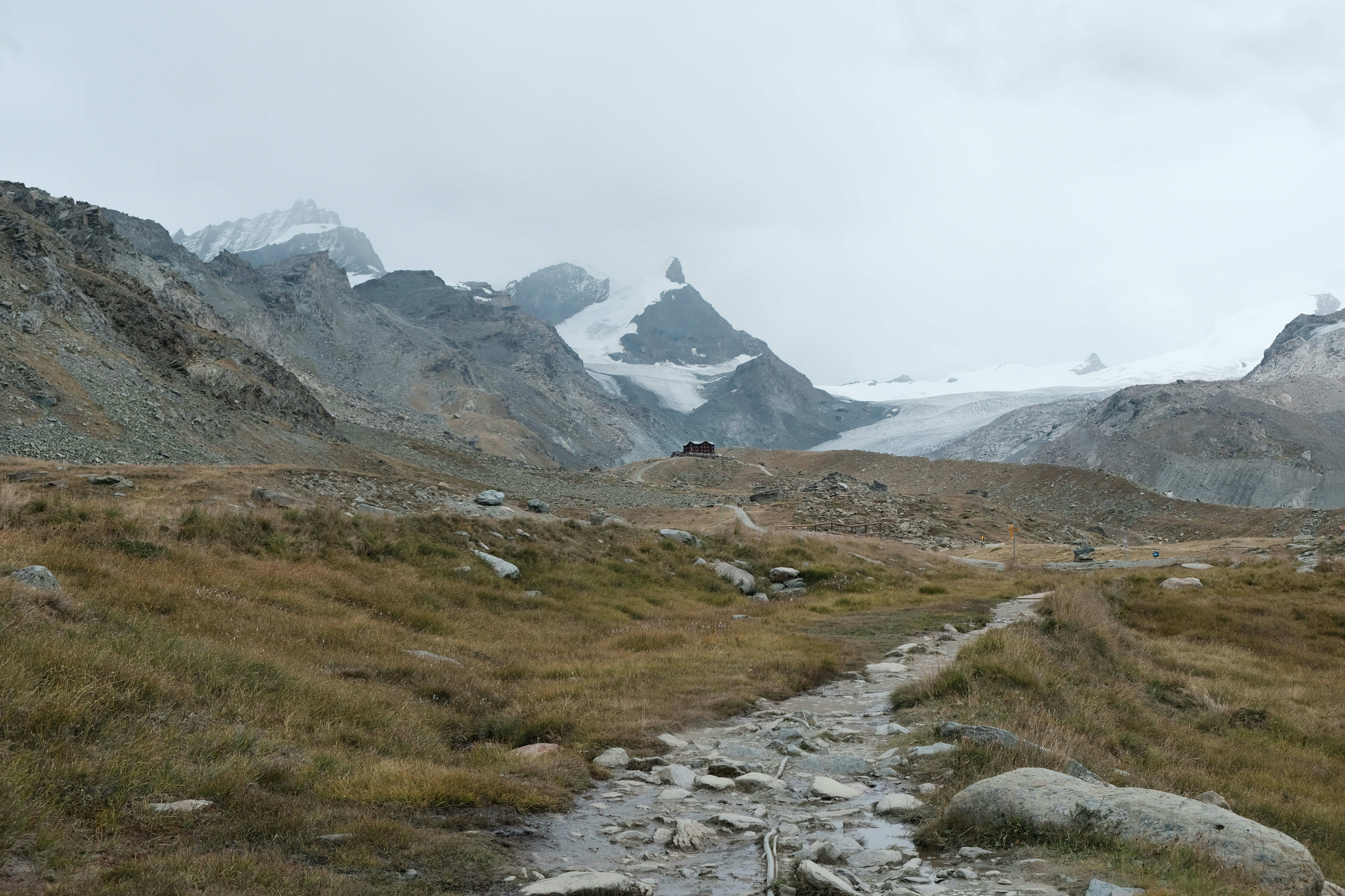 A rocky path leads through a grassy valley towards mountains.
