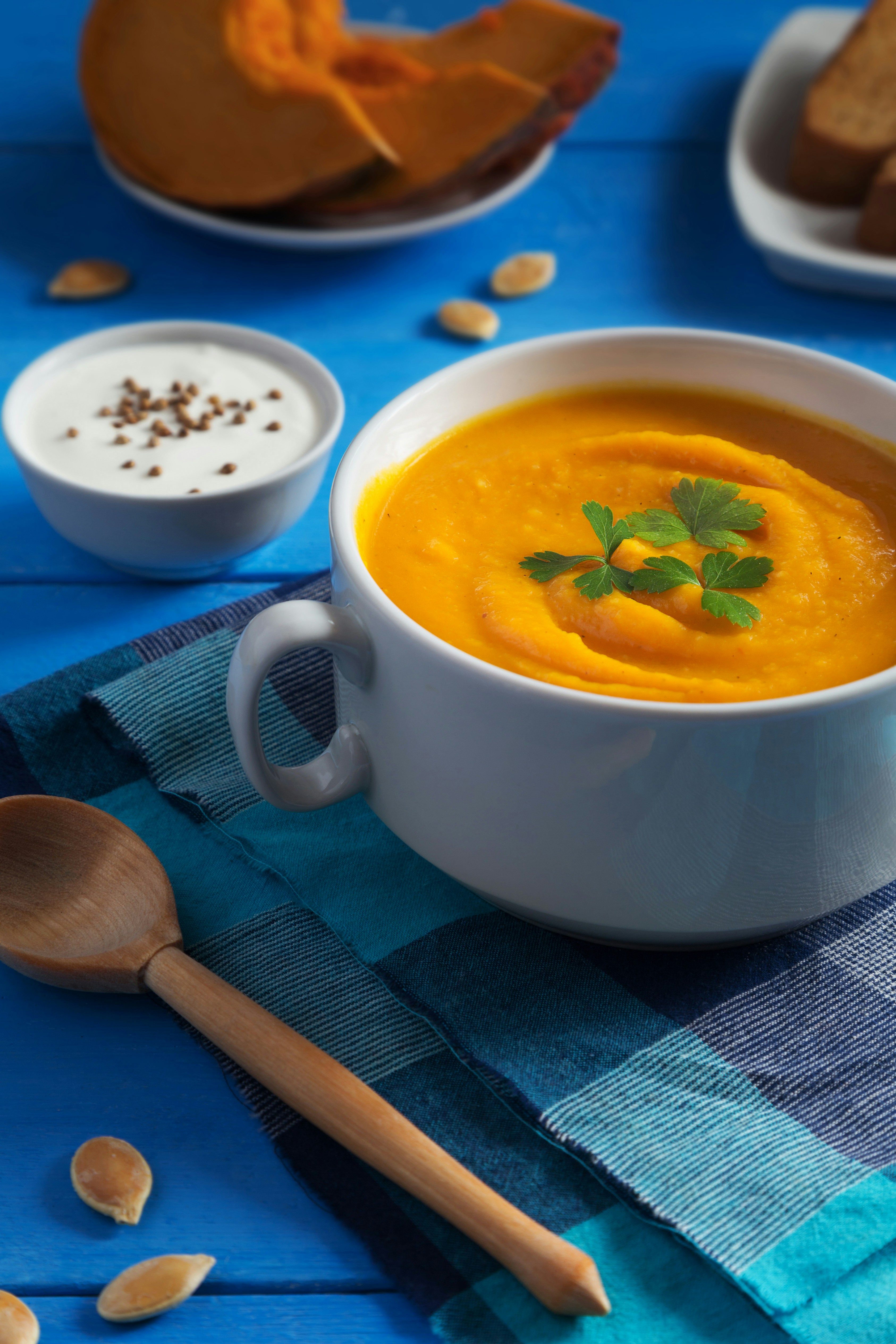 Vertical photo of pumpkin cream soup with seeds and croutons on blue background | Creamy pumpkin soup with parsley and bread