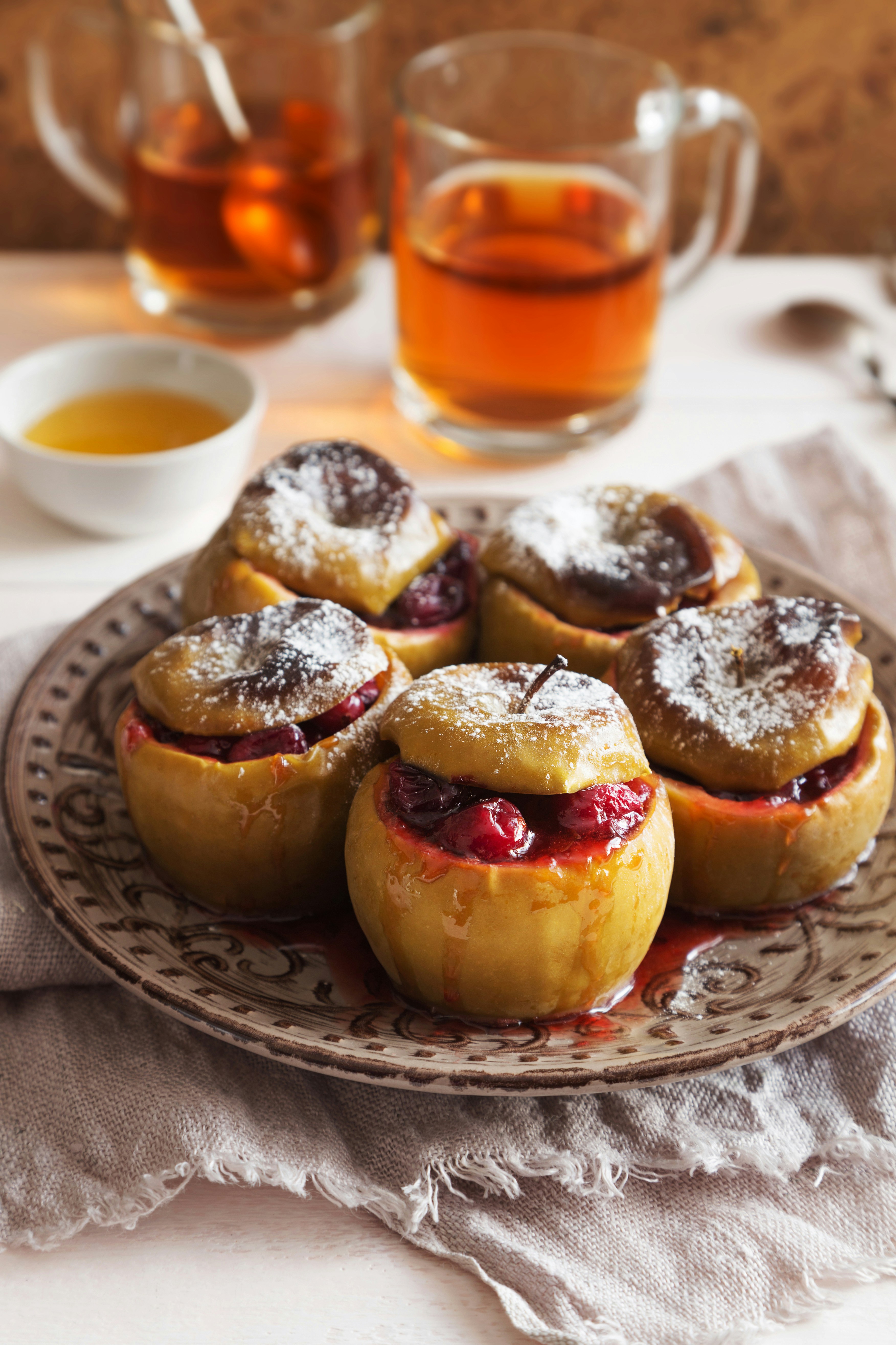 Vertical photo of a brown plate of baked apples with cranberries and tea | Baked apples filled with berries and dusted with powdered sugar.