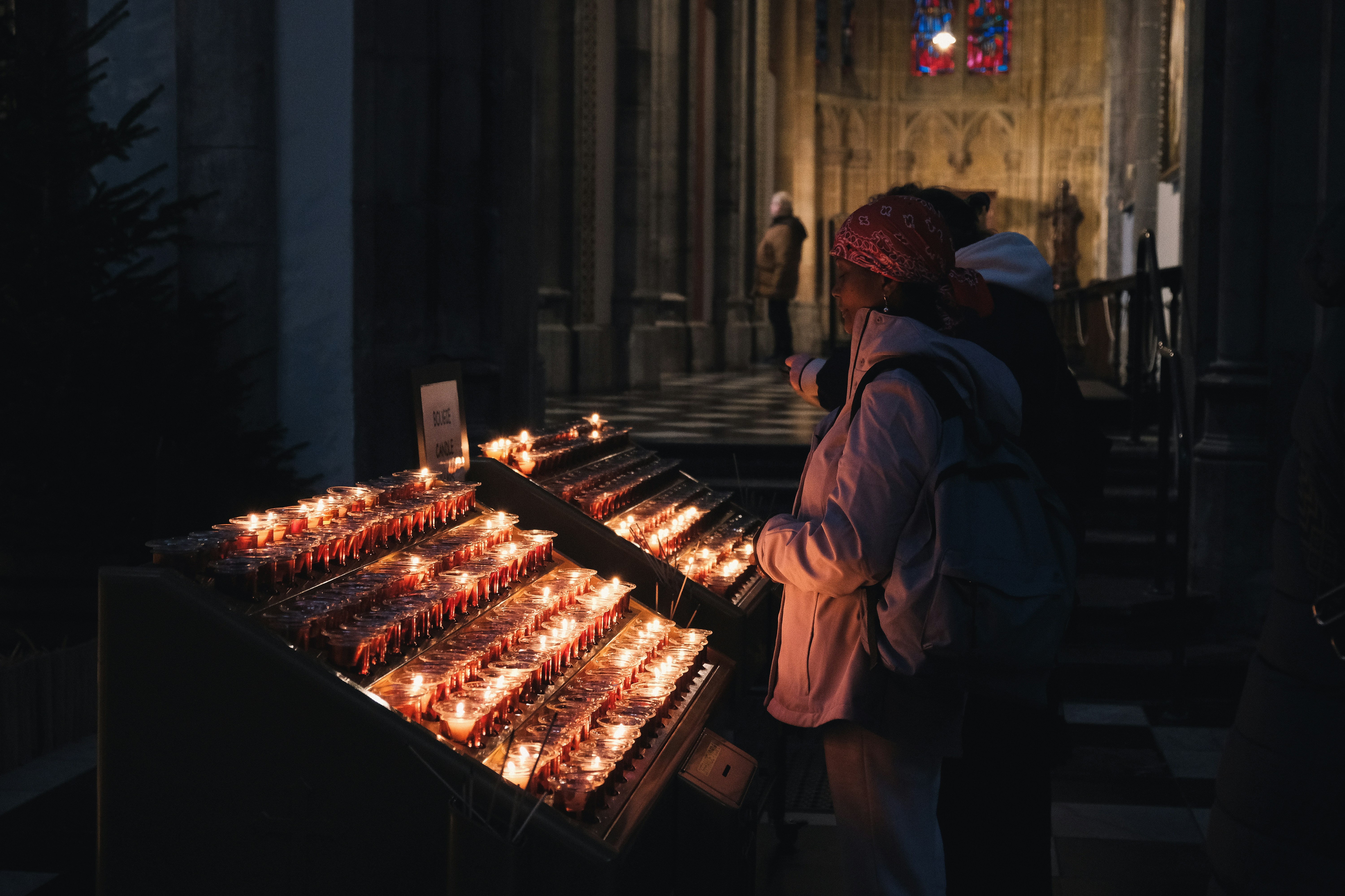 Woman lighting candles inside a dimly lit church.