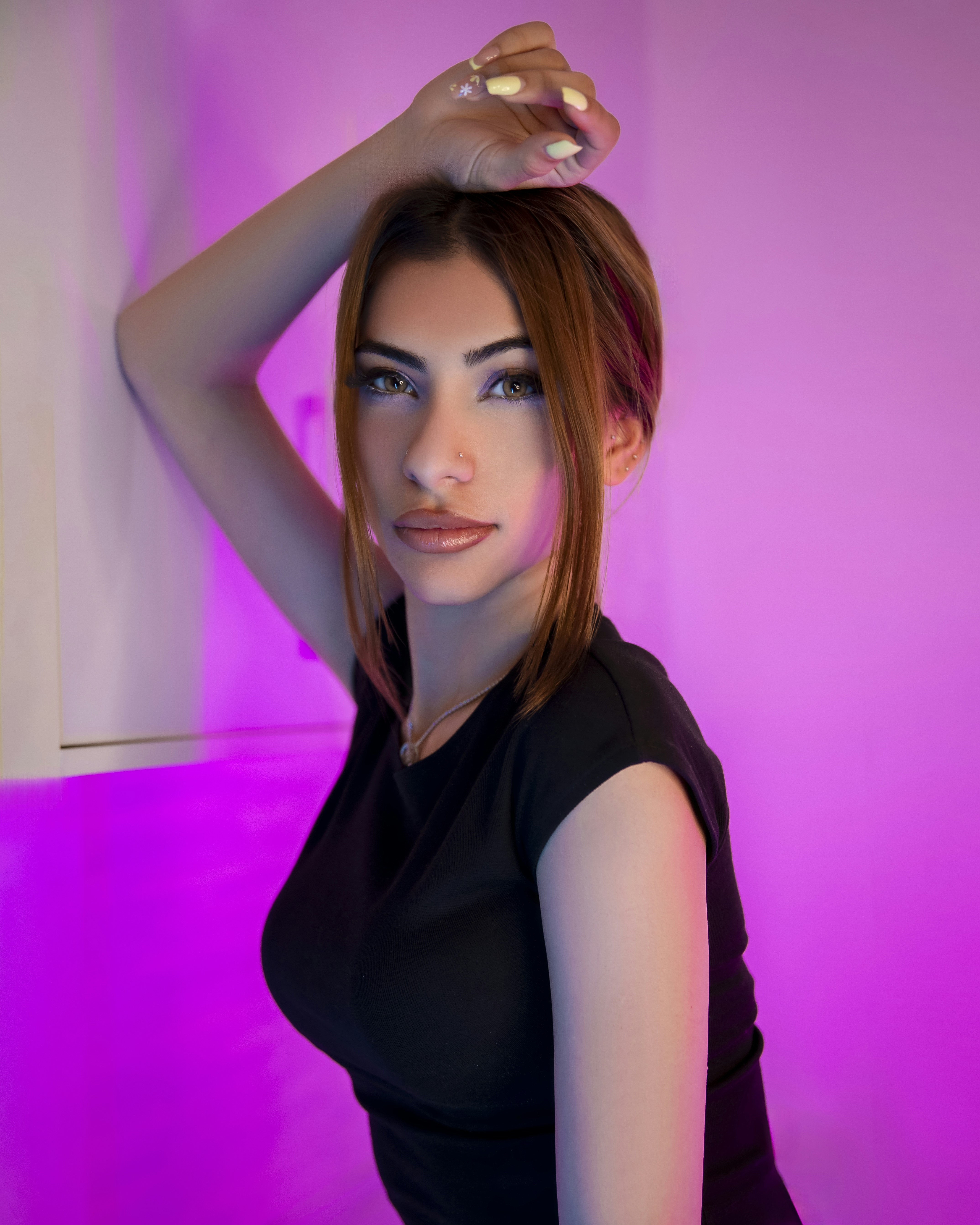Portrait photography of beautiful girl | A young woman poses with her arm raised against pink lighting.