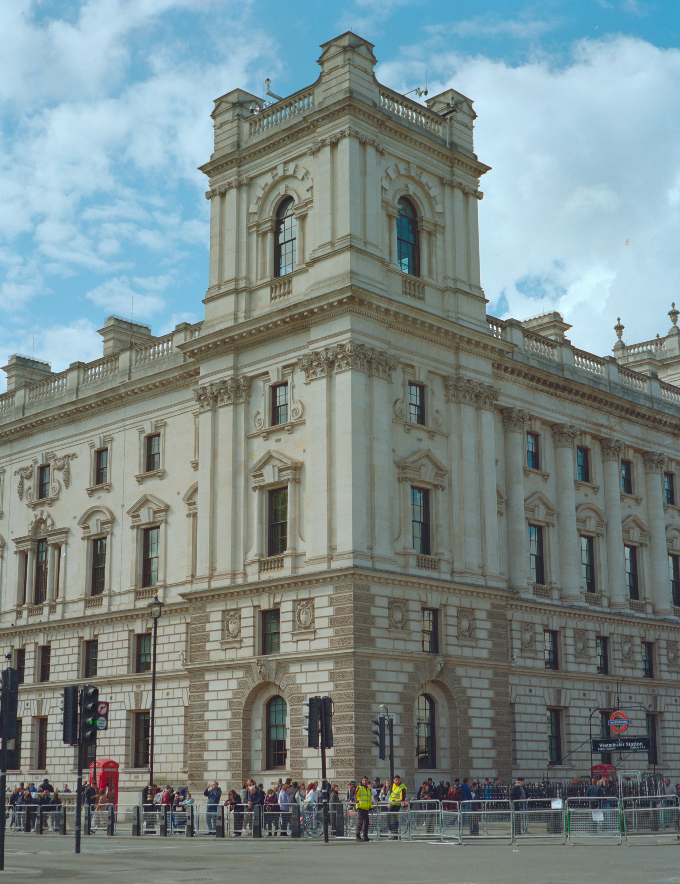 Historic government building with intricate stonework and large windows, bustling with people at the entrance.