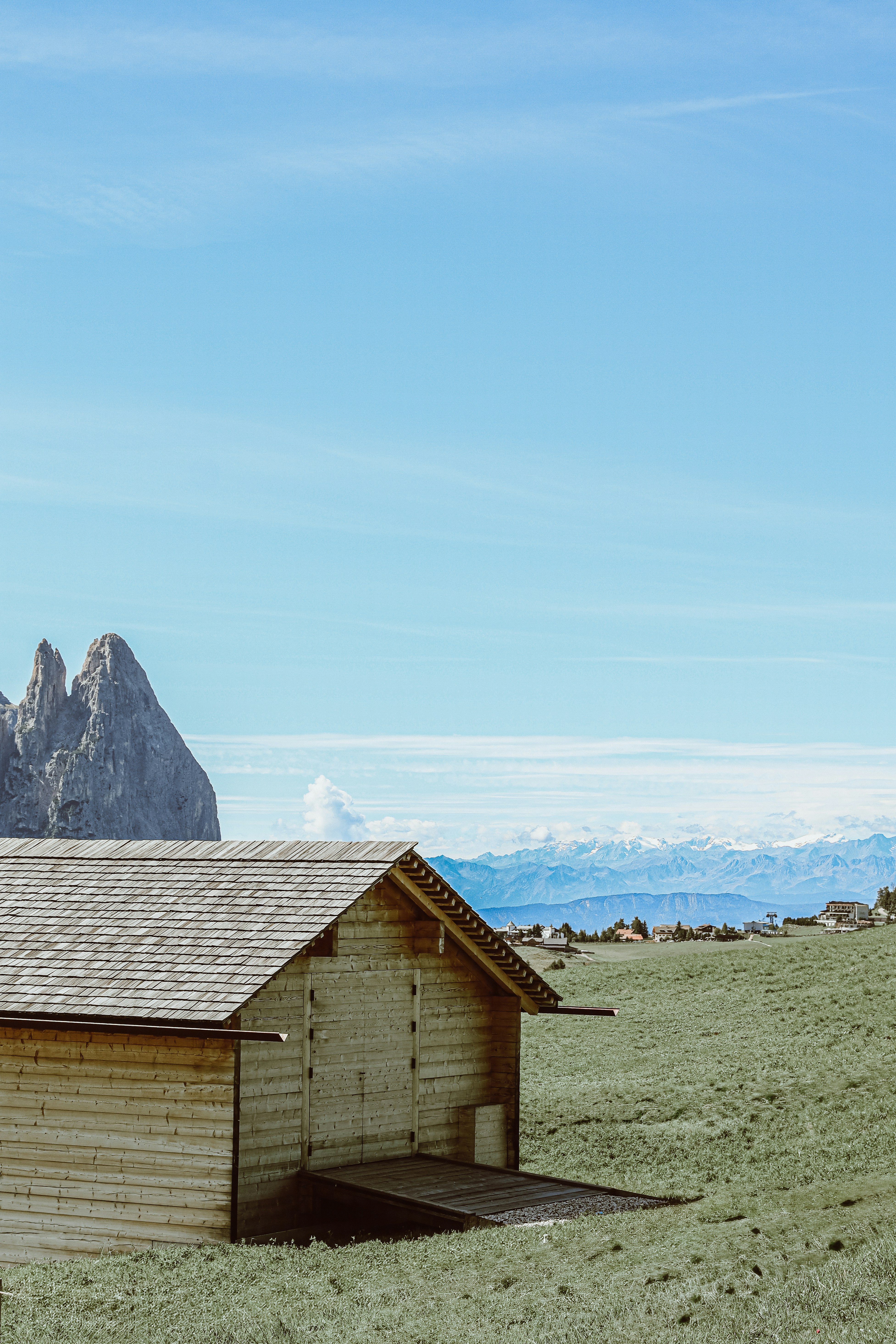 Wooden cabin in a grassy field with mountains.
