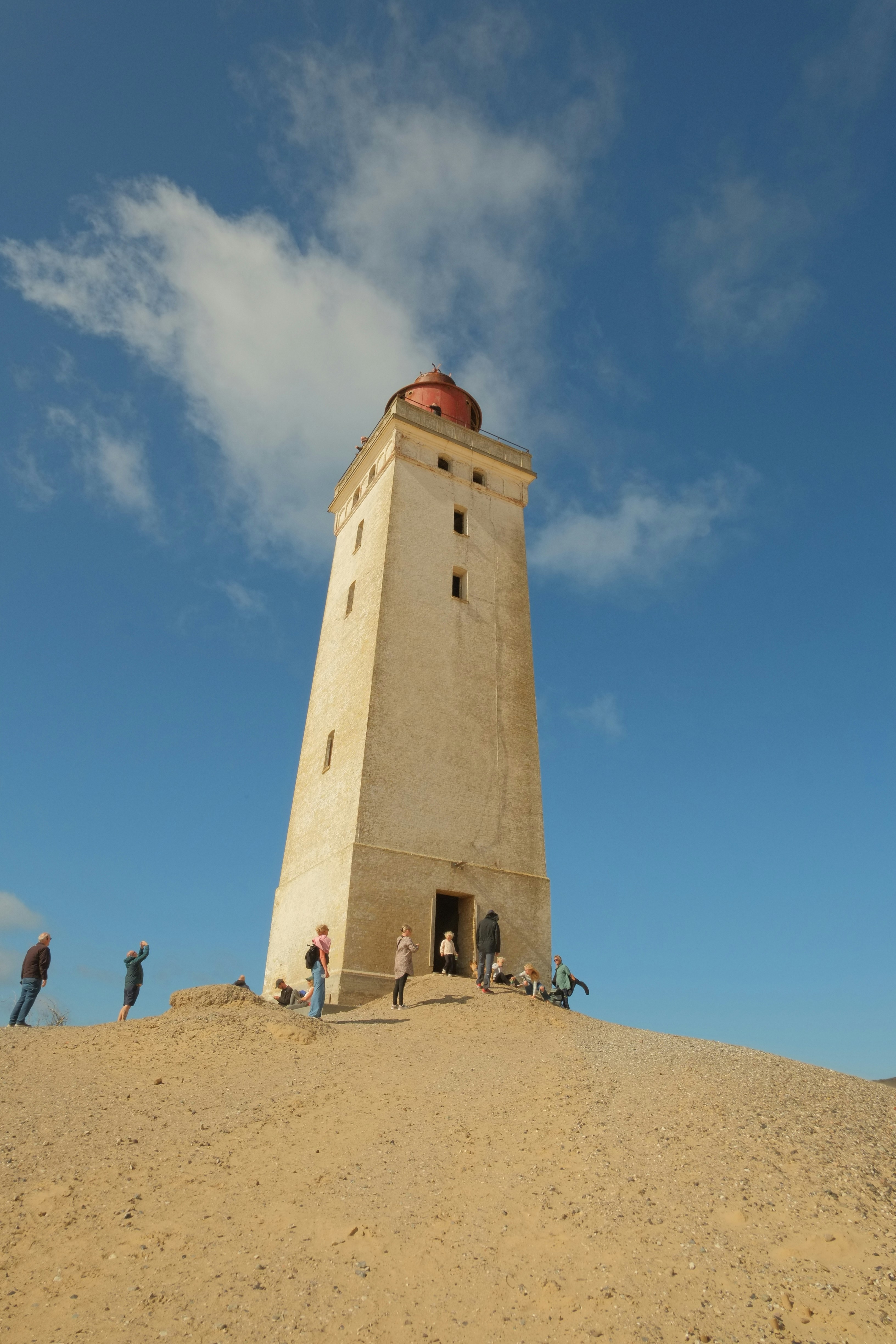 Tall lighthouse on a sandy dune under blue sky