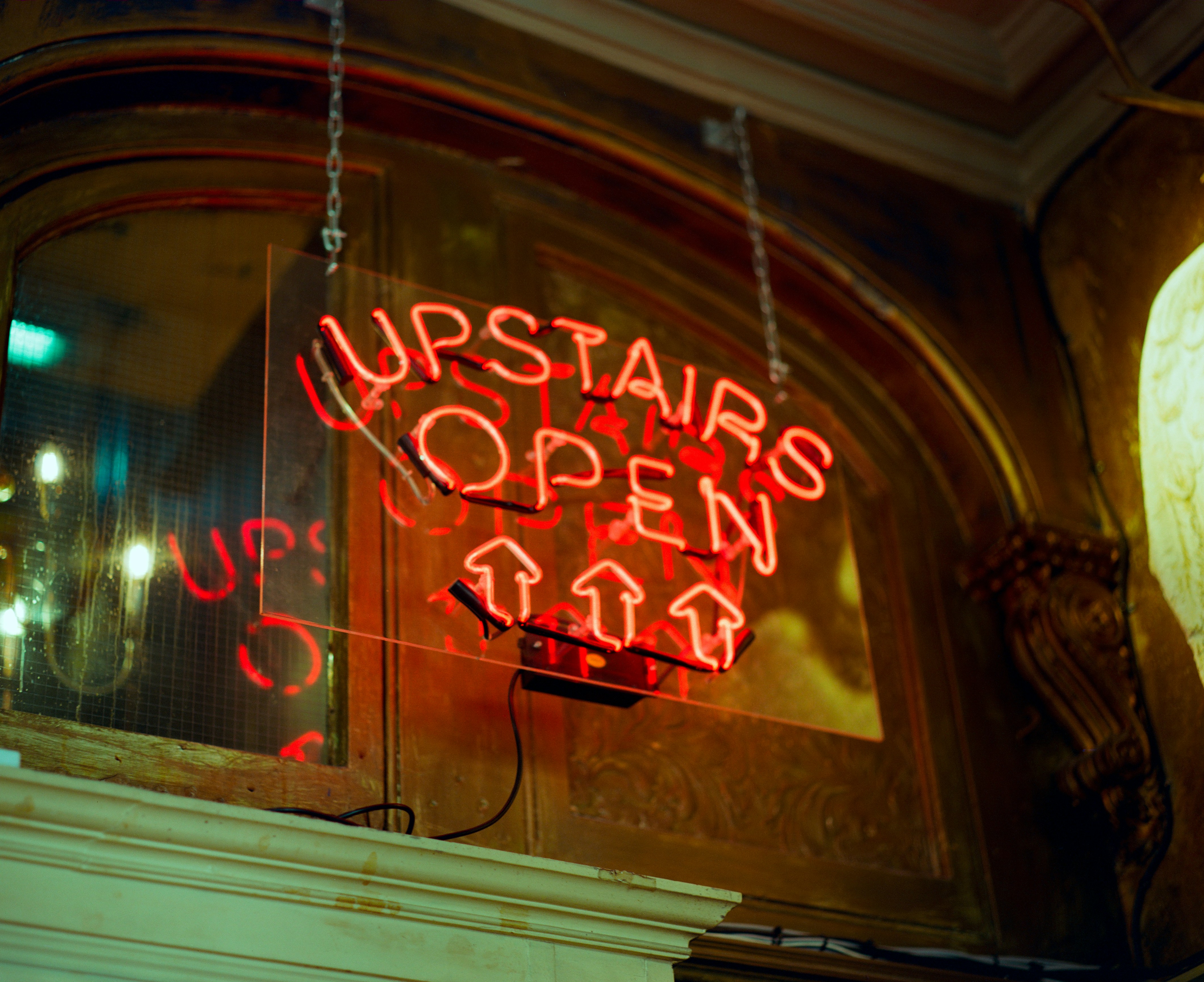 Neon sign reading 'UPSTAIRS OPEN' with arrows, glowing against an ornate background. The vibrant colors draw attention to the message.