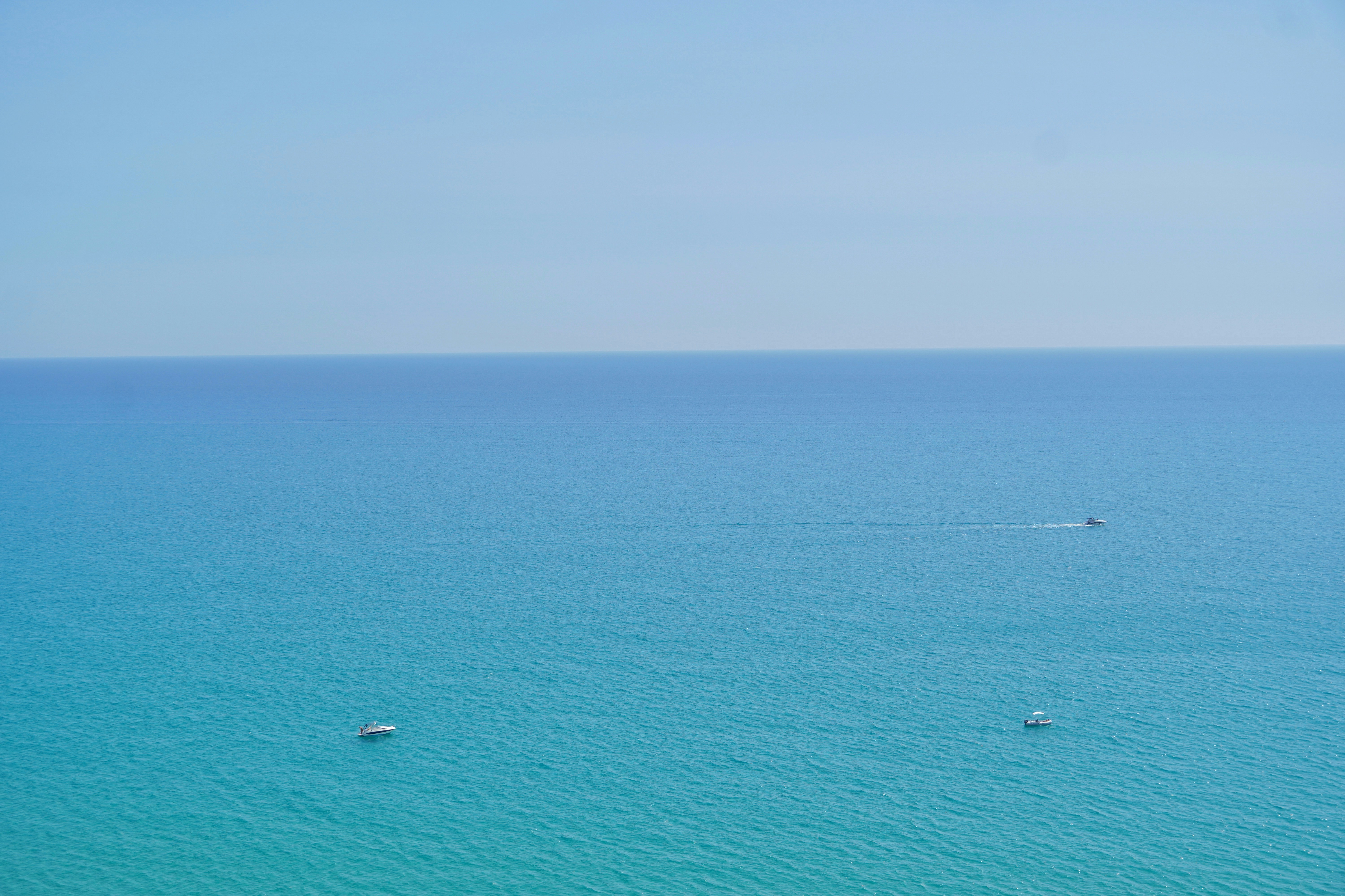 Three small boats sail on a vast blue ocean.