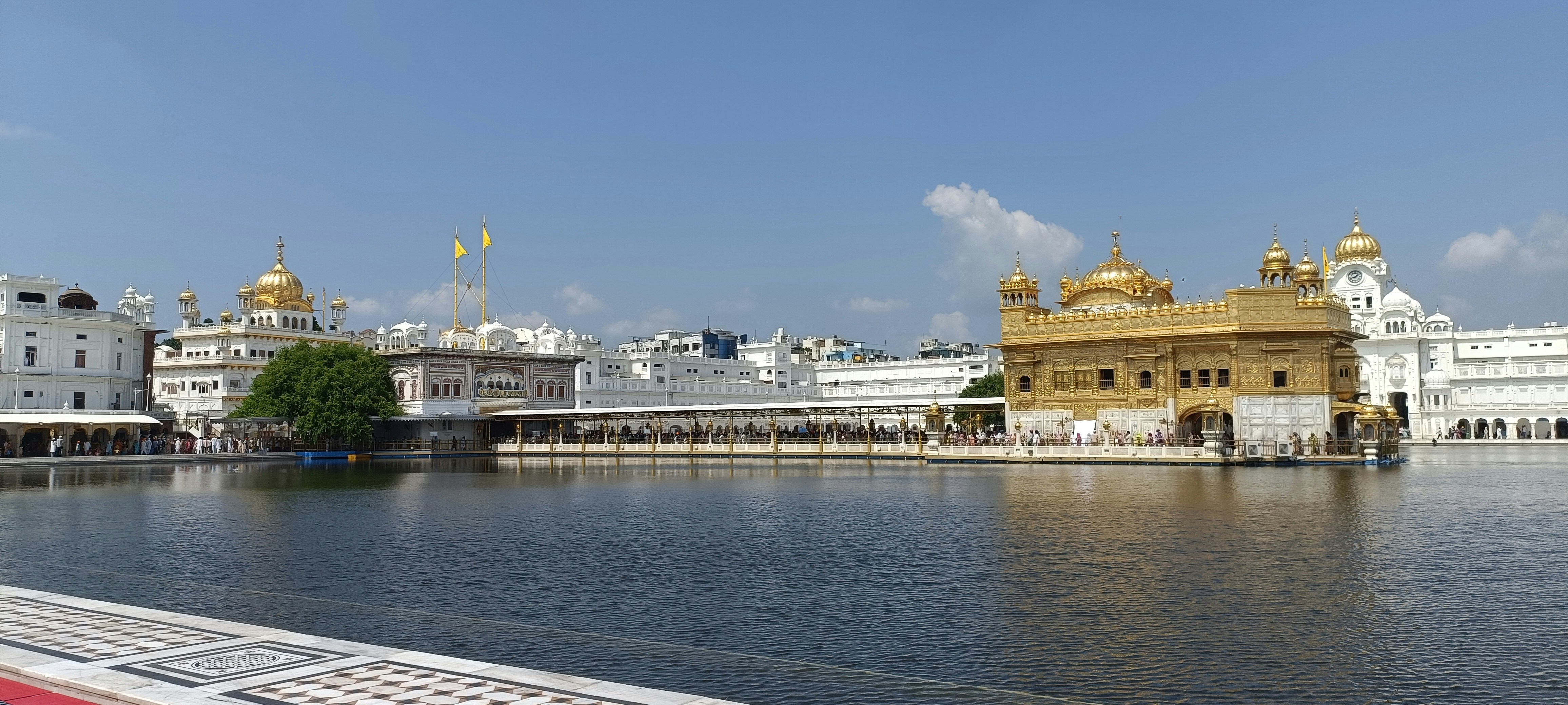 Golden Temple surrounded by serene waters, with intricate architecture and vibrant flags fluttering under a clear blue sky.