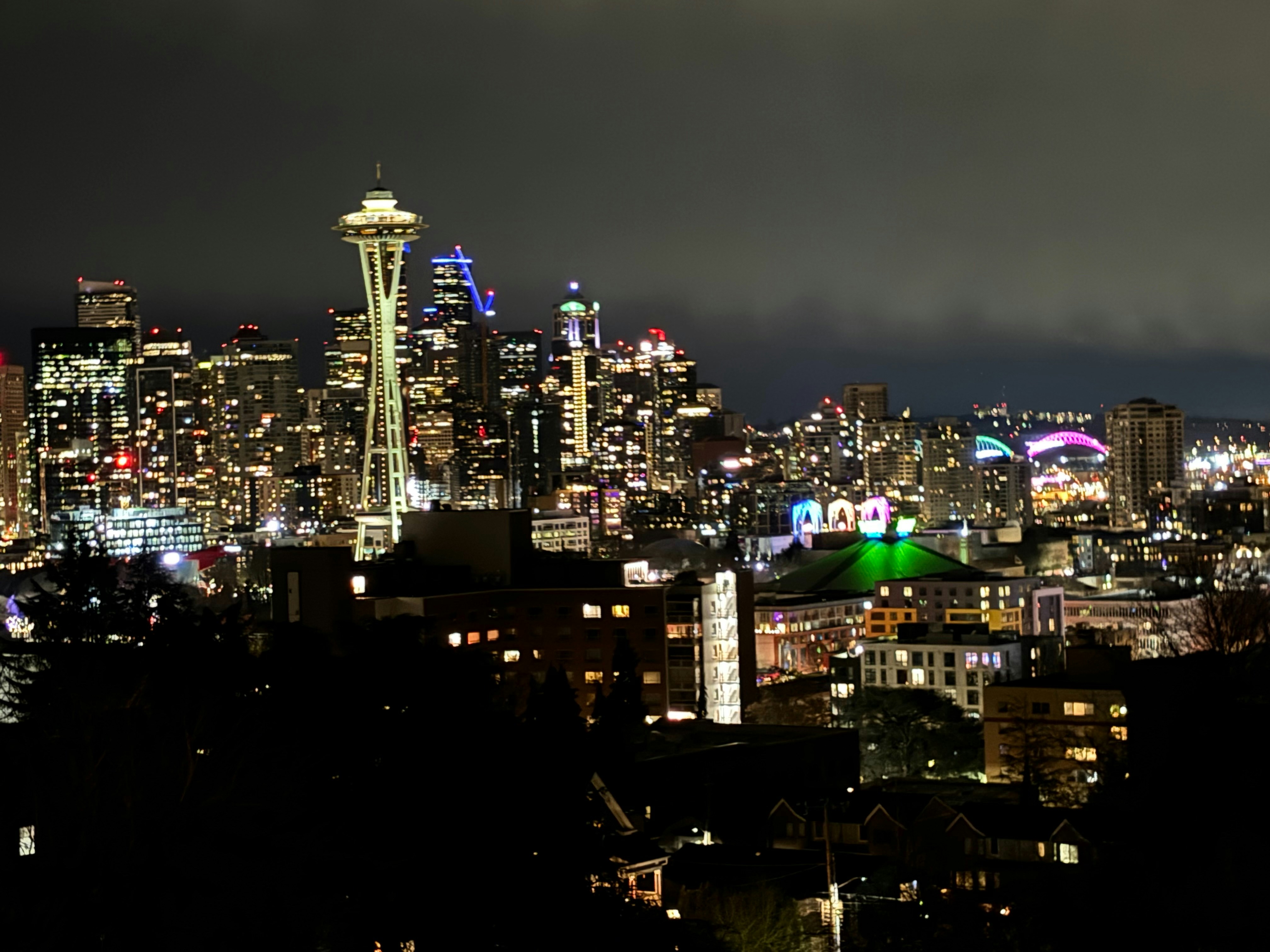 Vibrant cityscape of Seattle illuminated at night, featuring the iconic Space Needle and colorful buildings. A blend of urban lights creates a dynamic atmosphere.