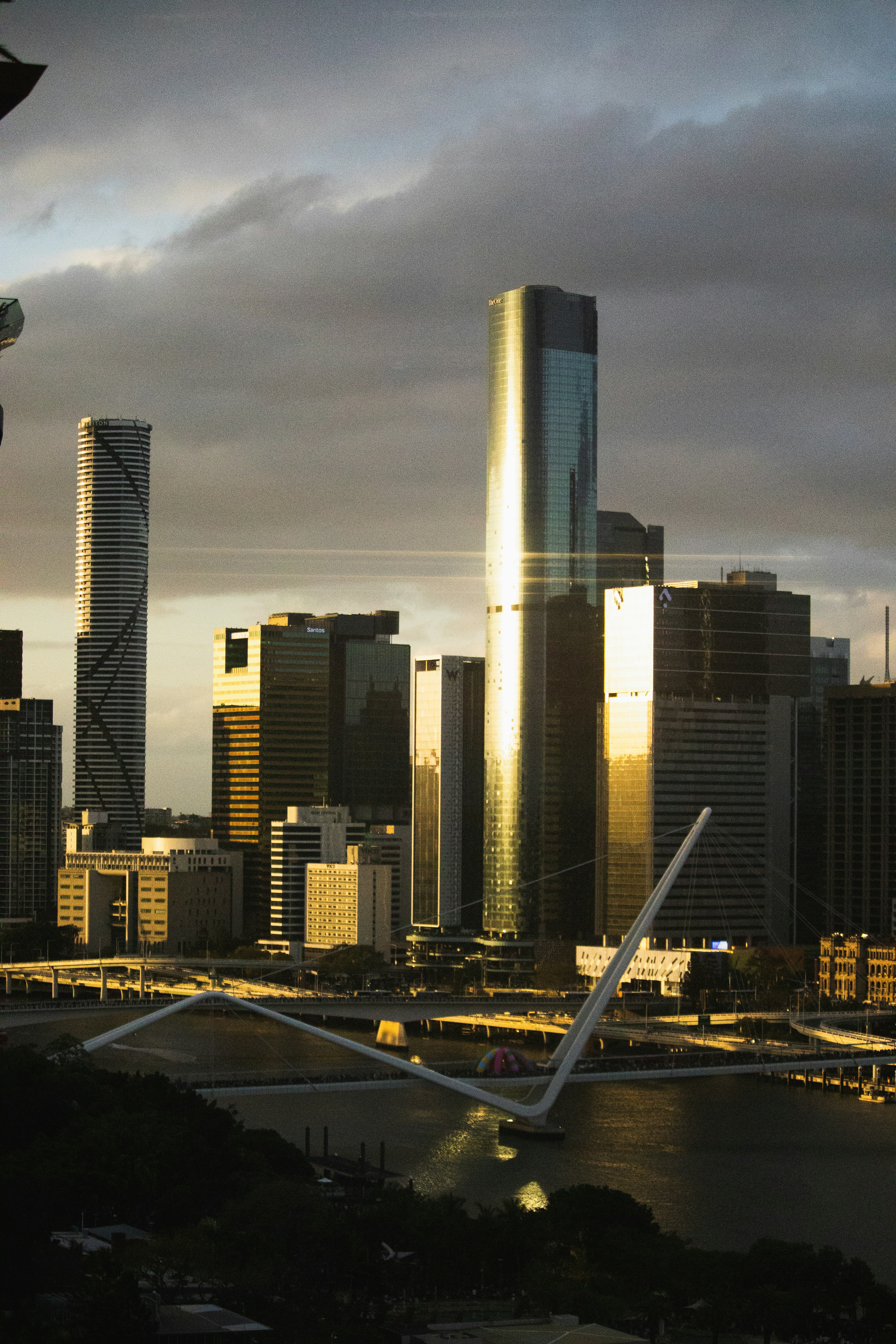 City skyline featuring reflective skyscrapers and a unique bridge over the water at sunset.