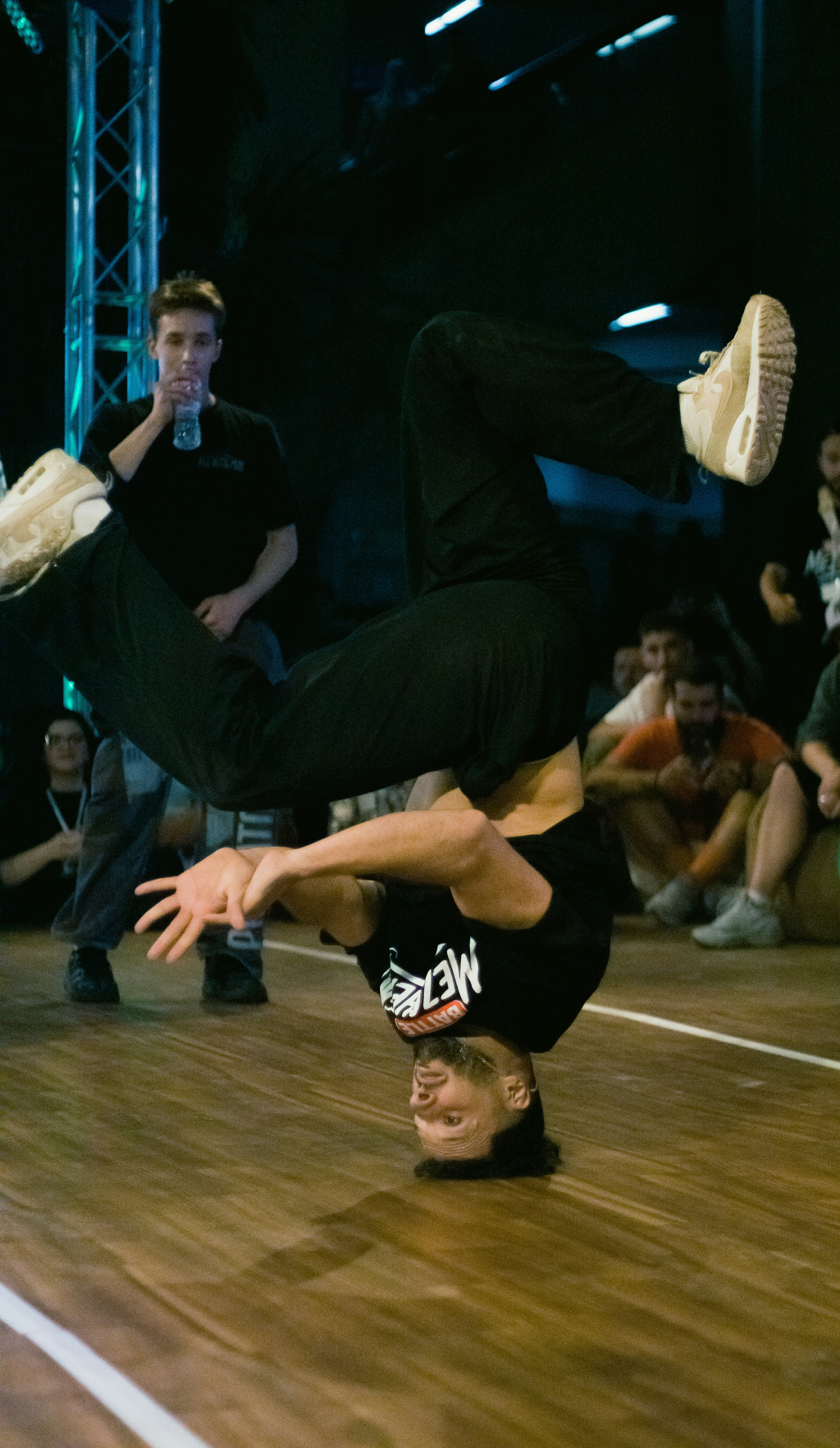 Breakdancer performs a headstand move on a wooden floor.