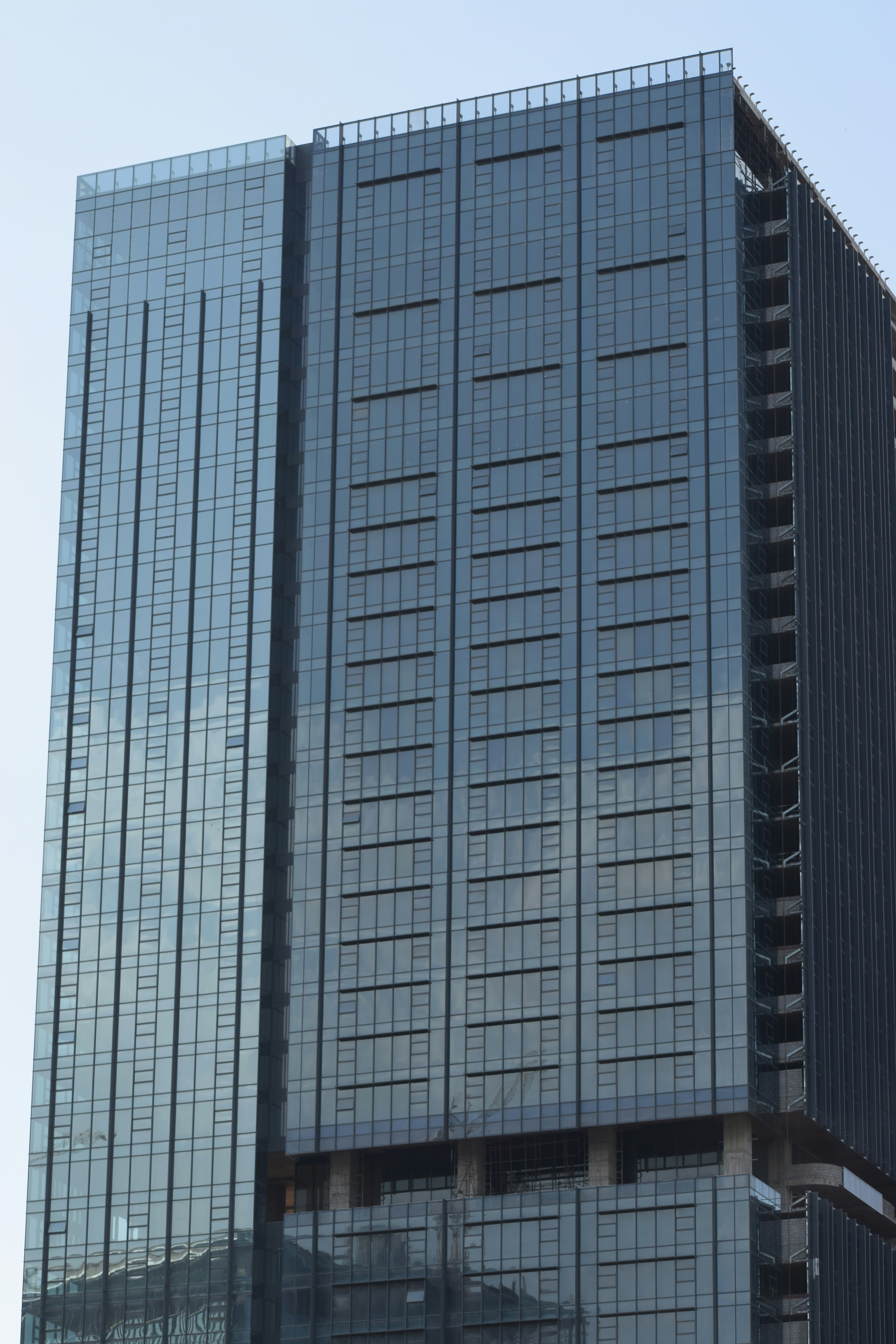 Tall glass skyscraper showcasing modern architecture with reflective surfaces and a partially completed structure.