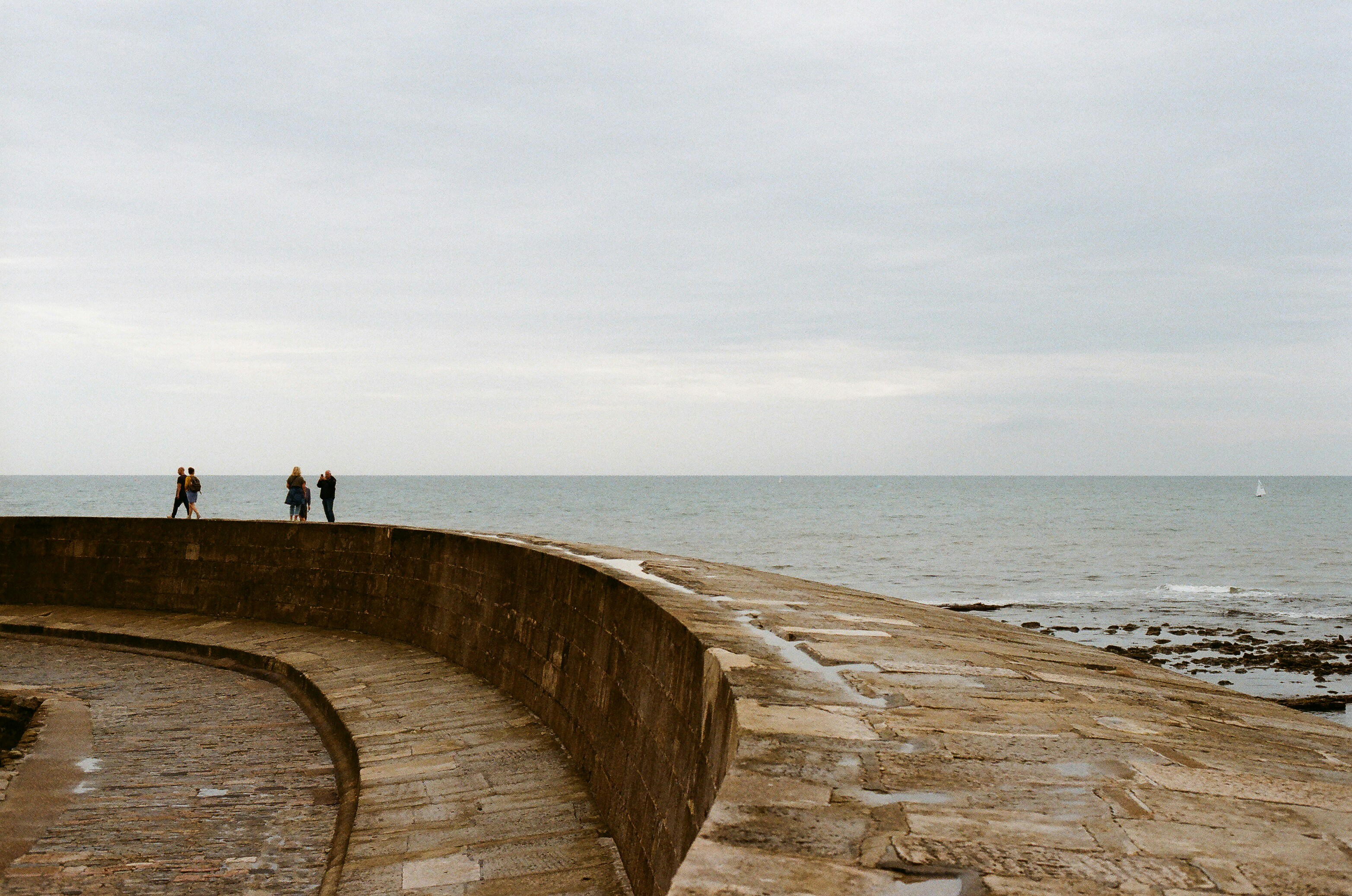 People walk on a curved stone walkway by the ocean. photo – Free Film ...
