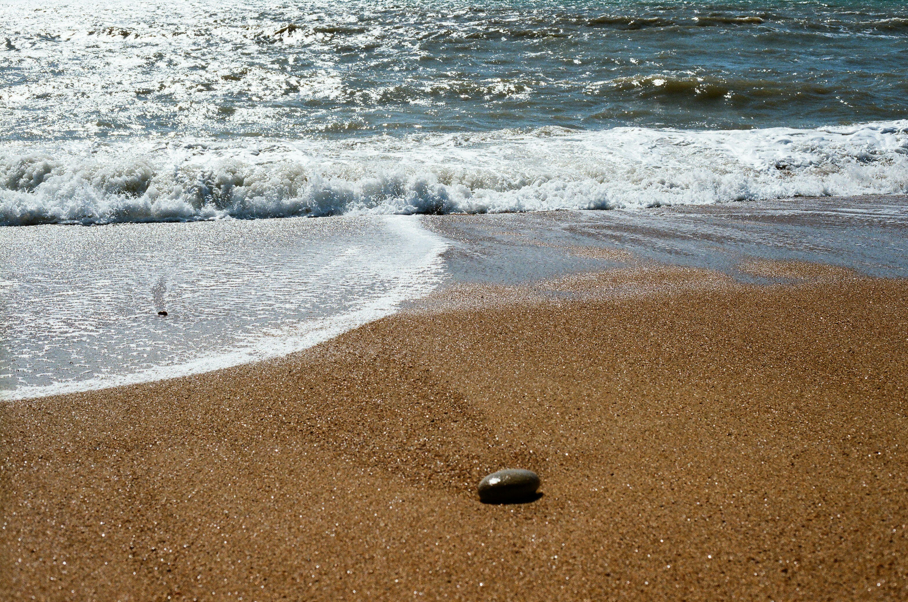 A single pebble rests on a sandy beach with waves. photo – Free Film ...