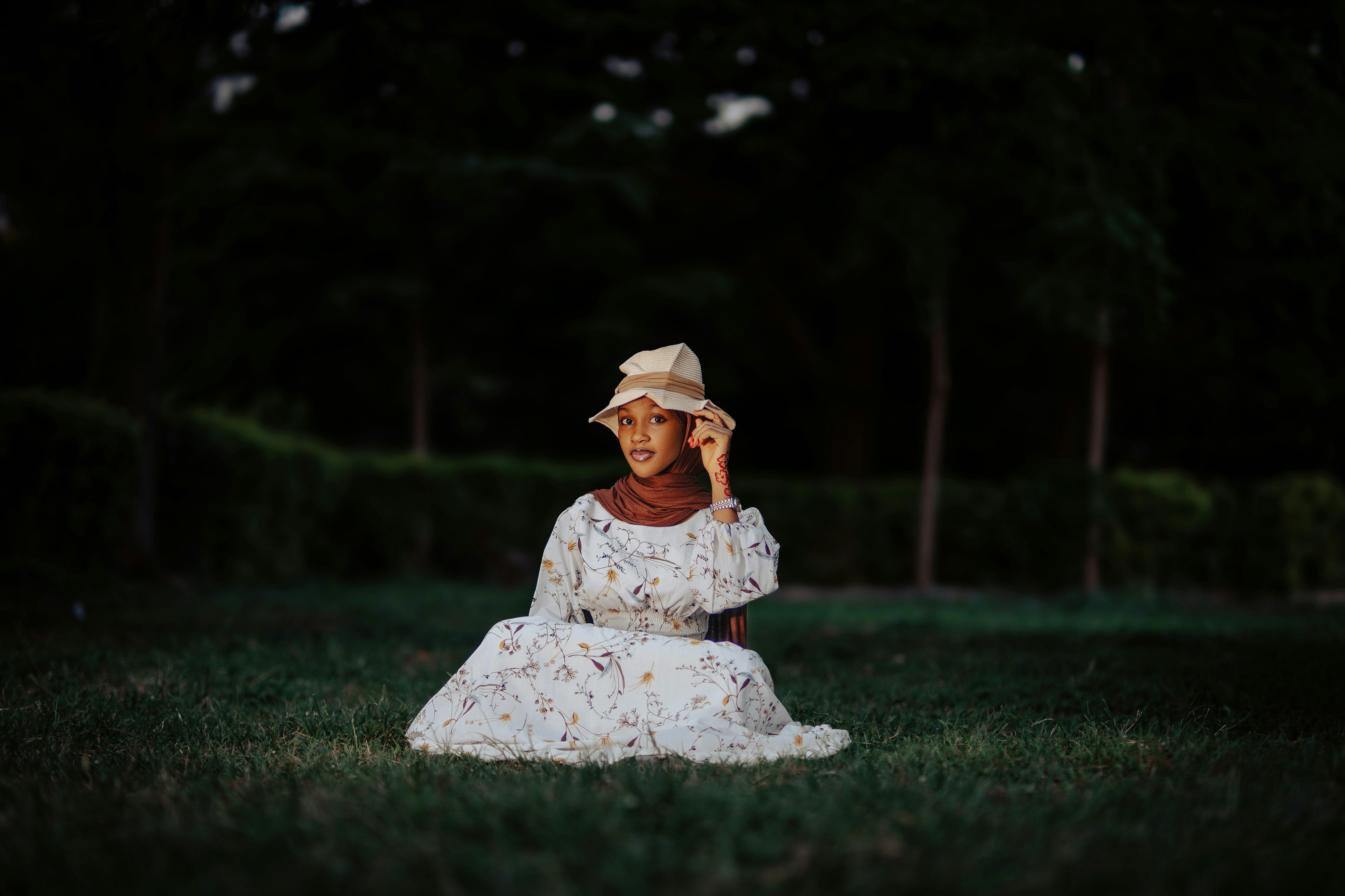 A minimalist shot of natural light falling across a textured surface, highlighting calm tones and details. | Woman in a hat and dress sitting on grass
