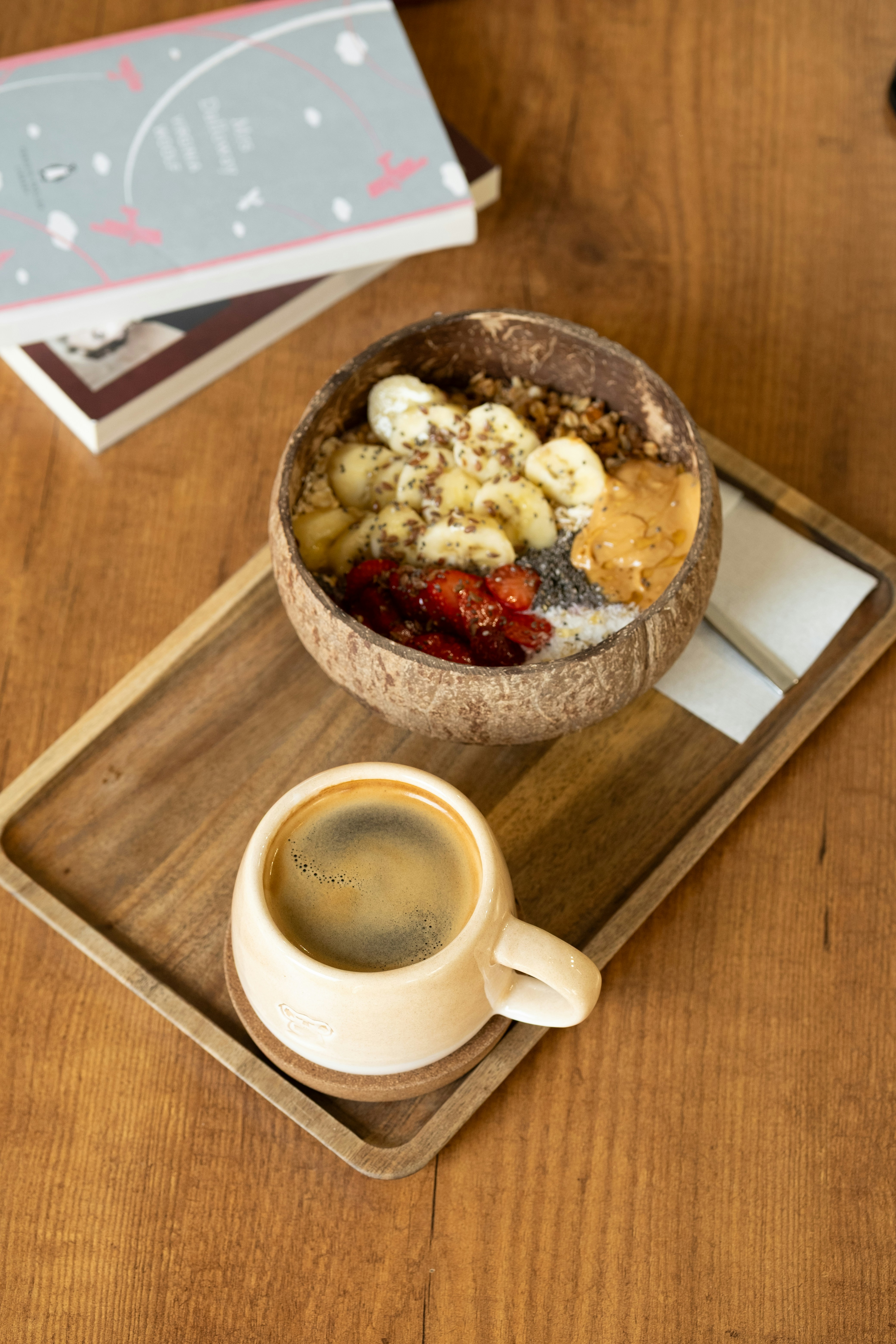 Coconut bowl with fruit, granola, and coffee on tray.