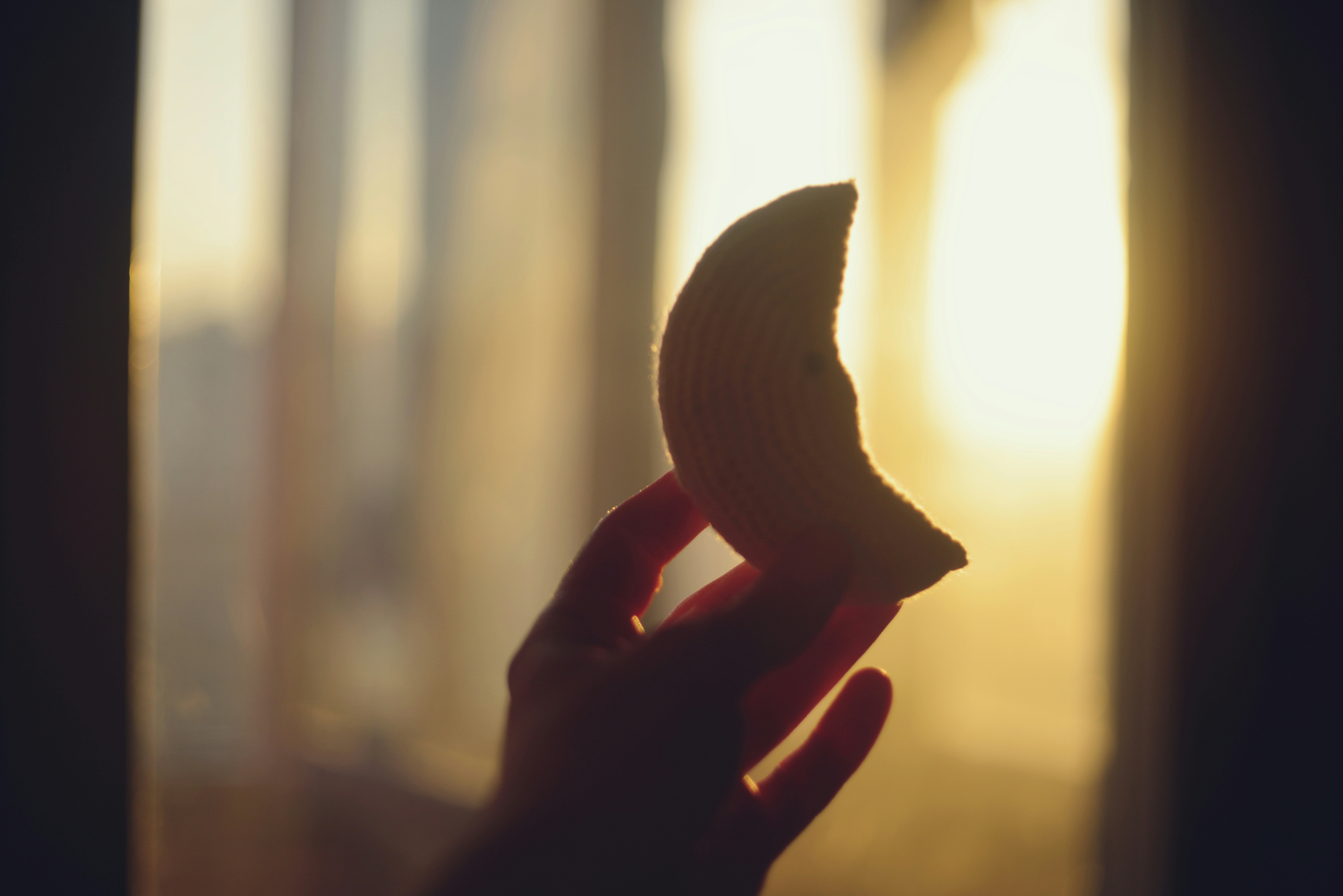 Hand holding crescent moon pastry against blurred window light.