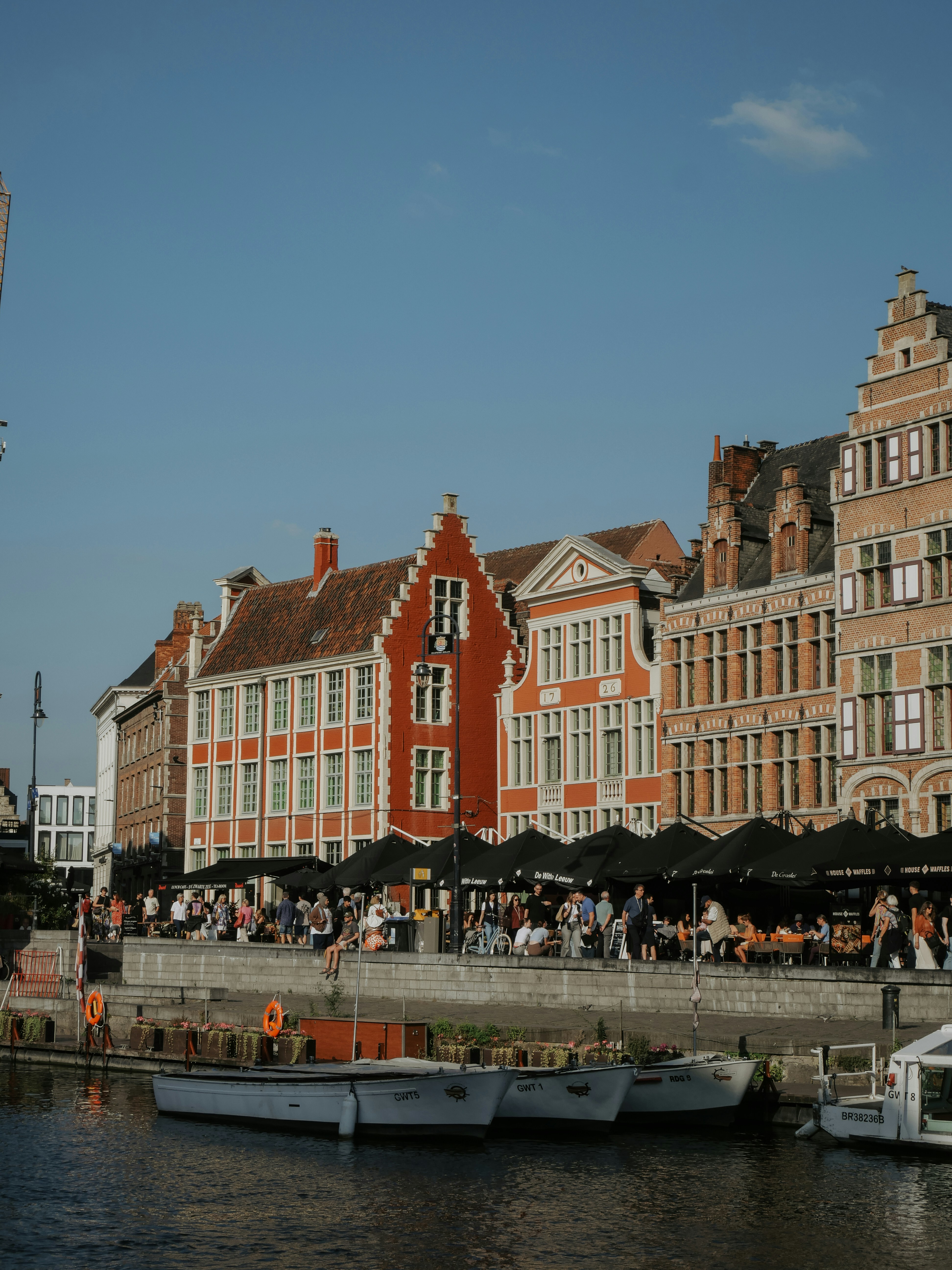Old harbour of Ghent | Boats on canal with buildings and people dining.