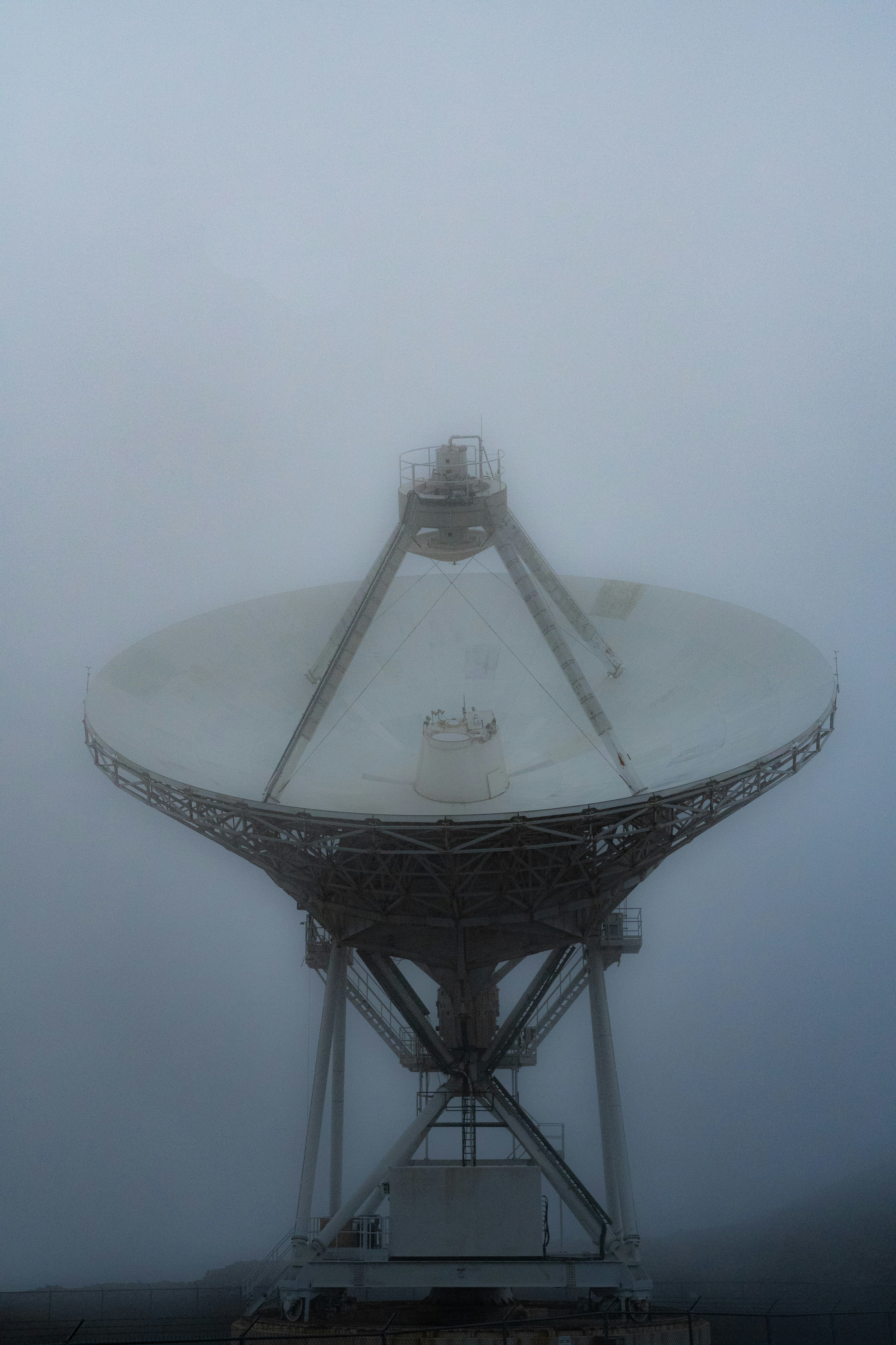 Large satellite dish shrouded in fog, highlighting its intricate structure and purpose in communication. The atmospheric conditions create a mysterious ambiance.