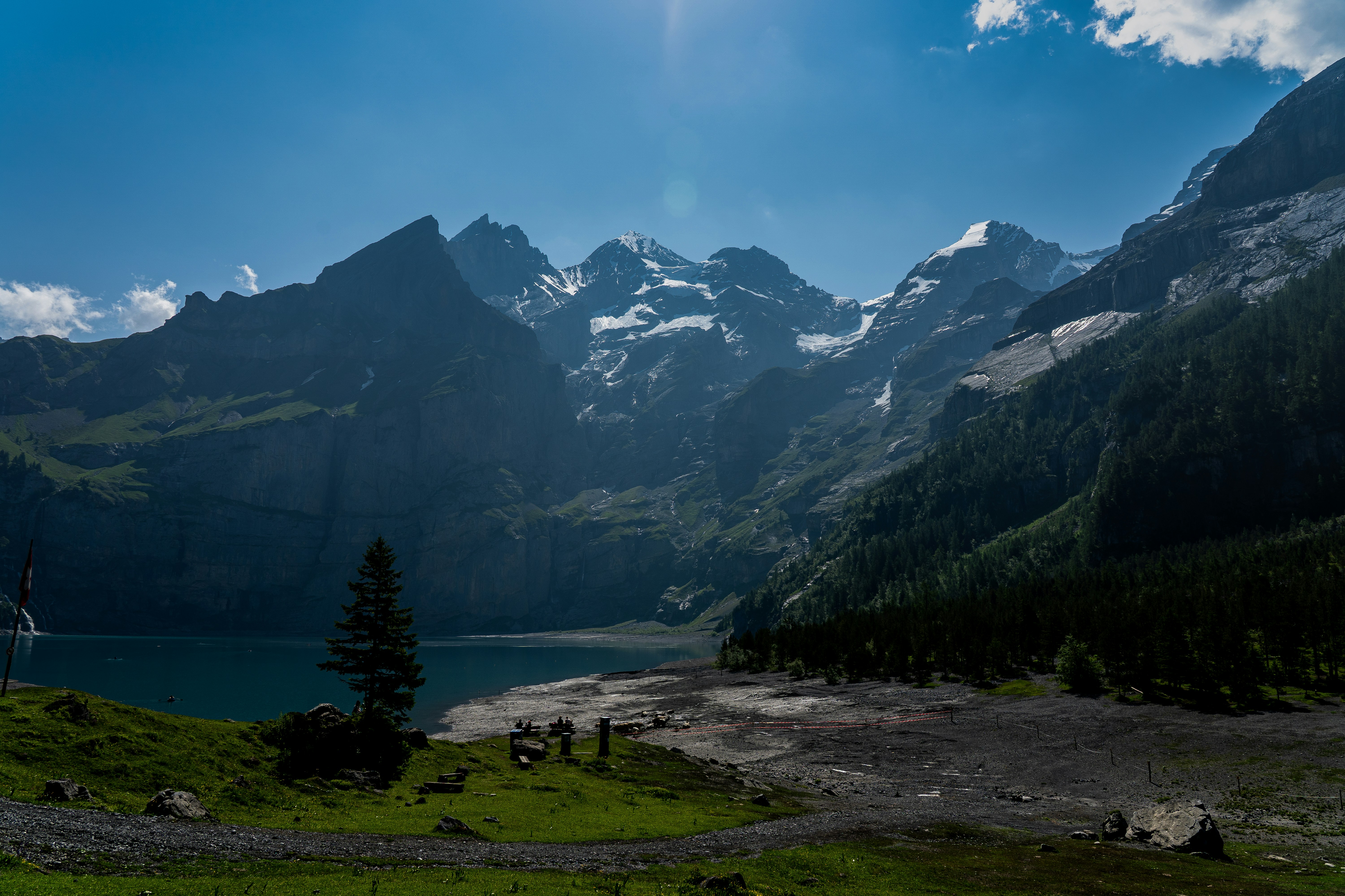 Majestic mountain range reflected in a serene lake, surrounded by lush greenery and rocky terrain. The scene captures the essence of untouched nature.