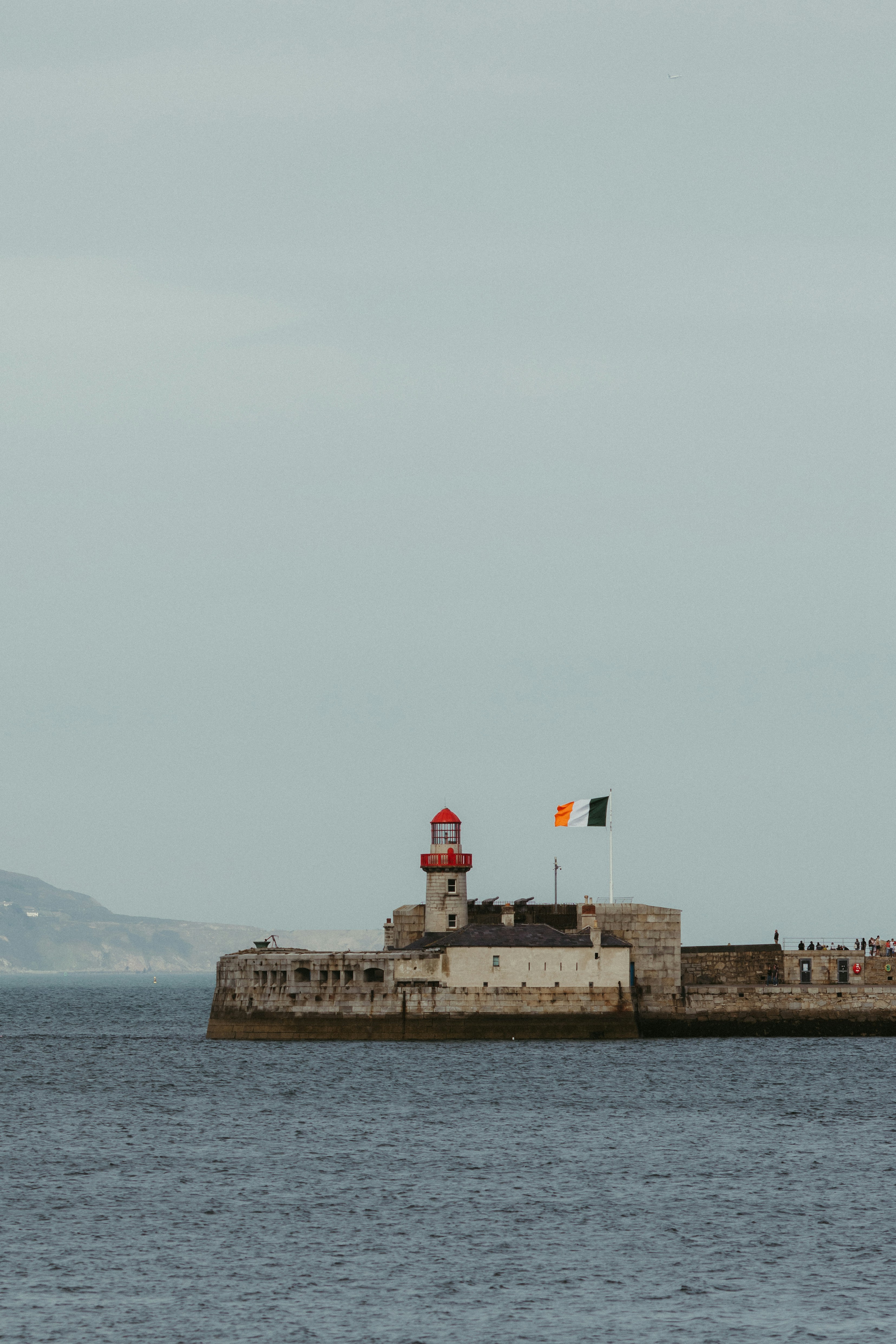 A lighthouse stands proudly on a rocky outcrop, with the Irish flag waving in the breeze against a serene ocean backdrop.