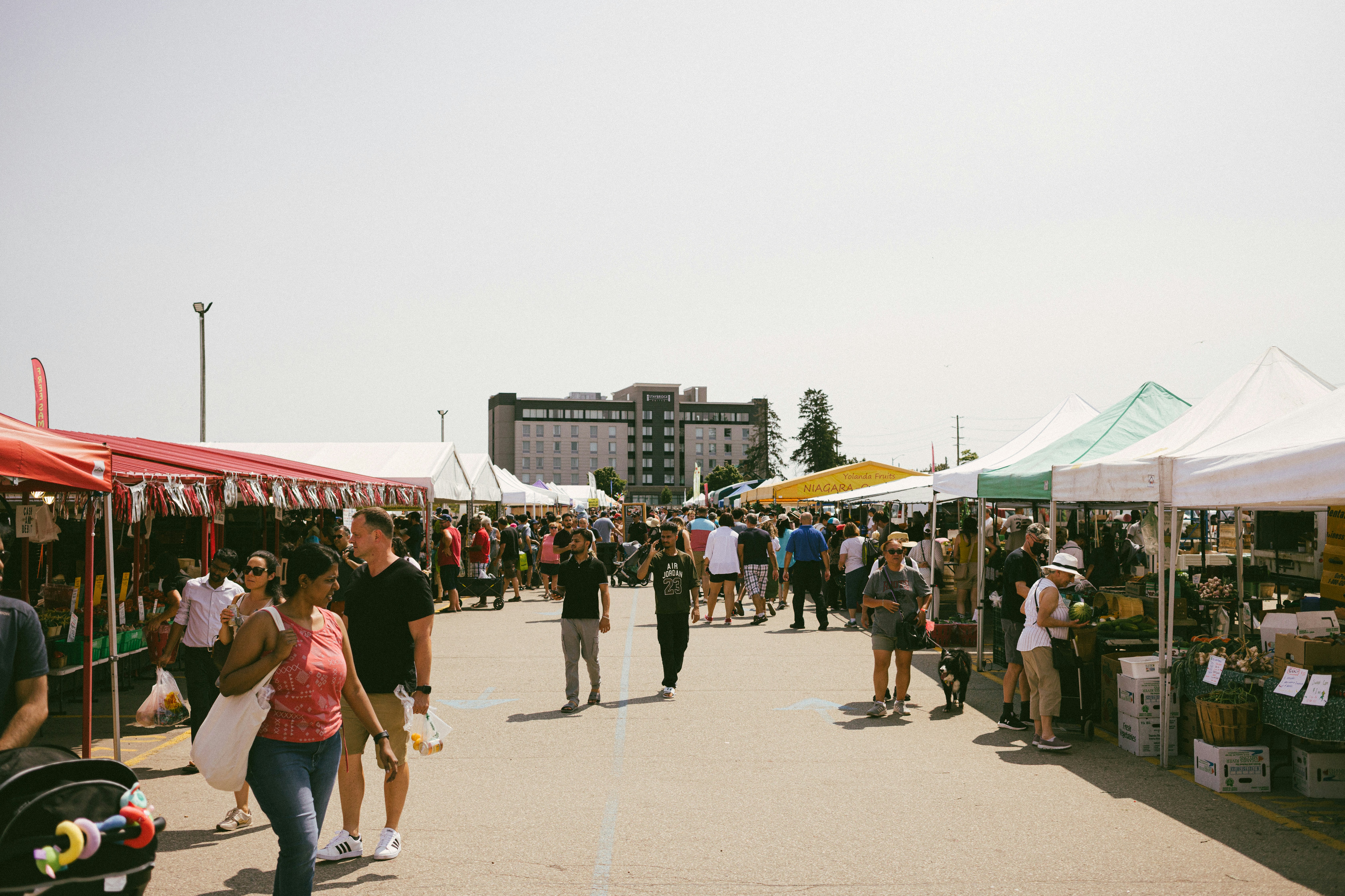 Sunlit Market Corridor: Tents, Foot Traffic, and a Distant City Block