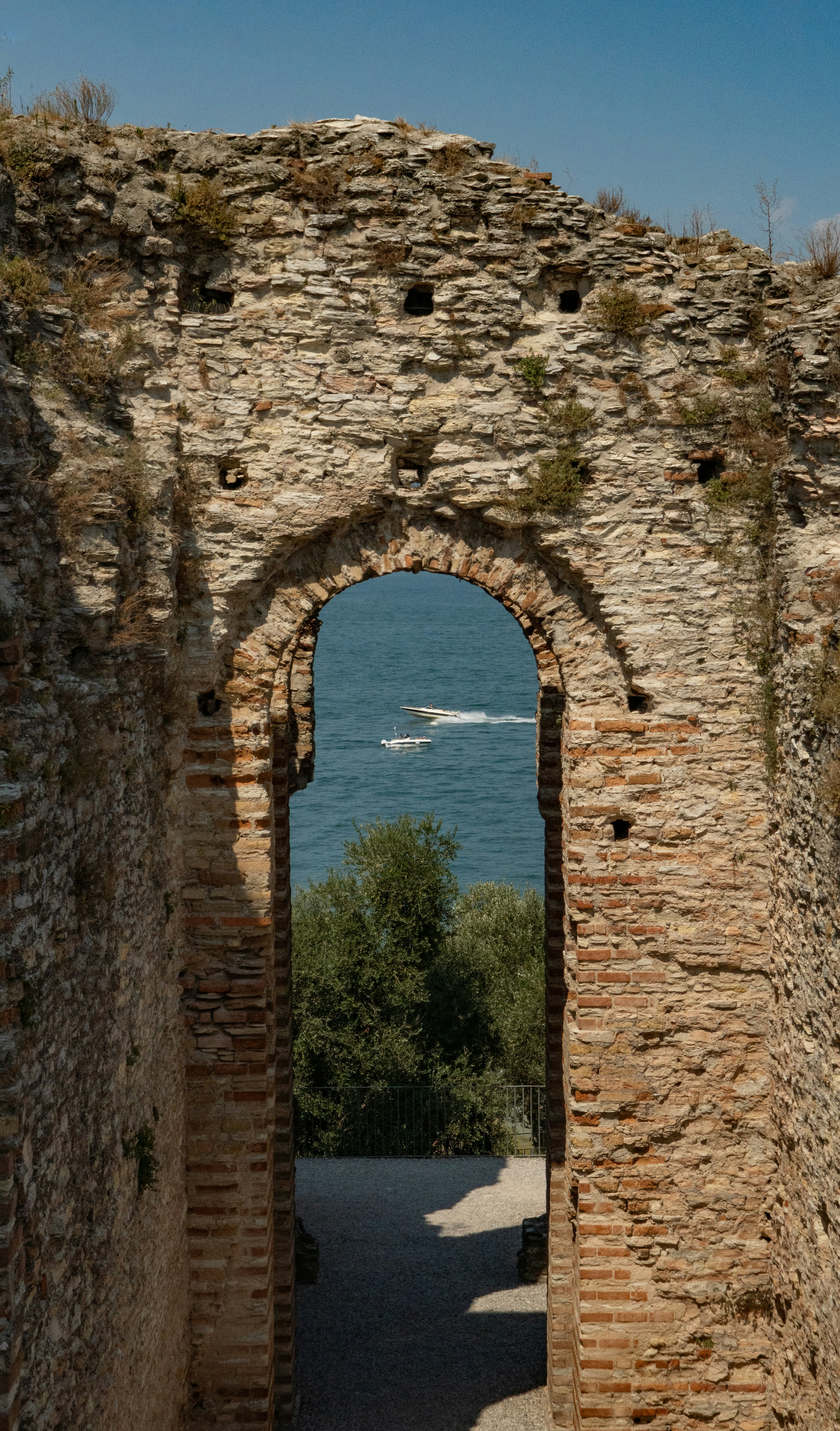 Ancient stone archway overlooking a blue ocean with boats.