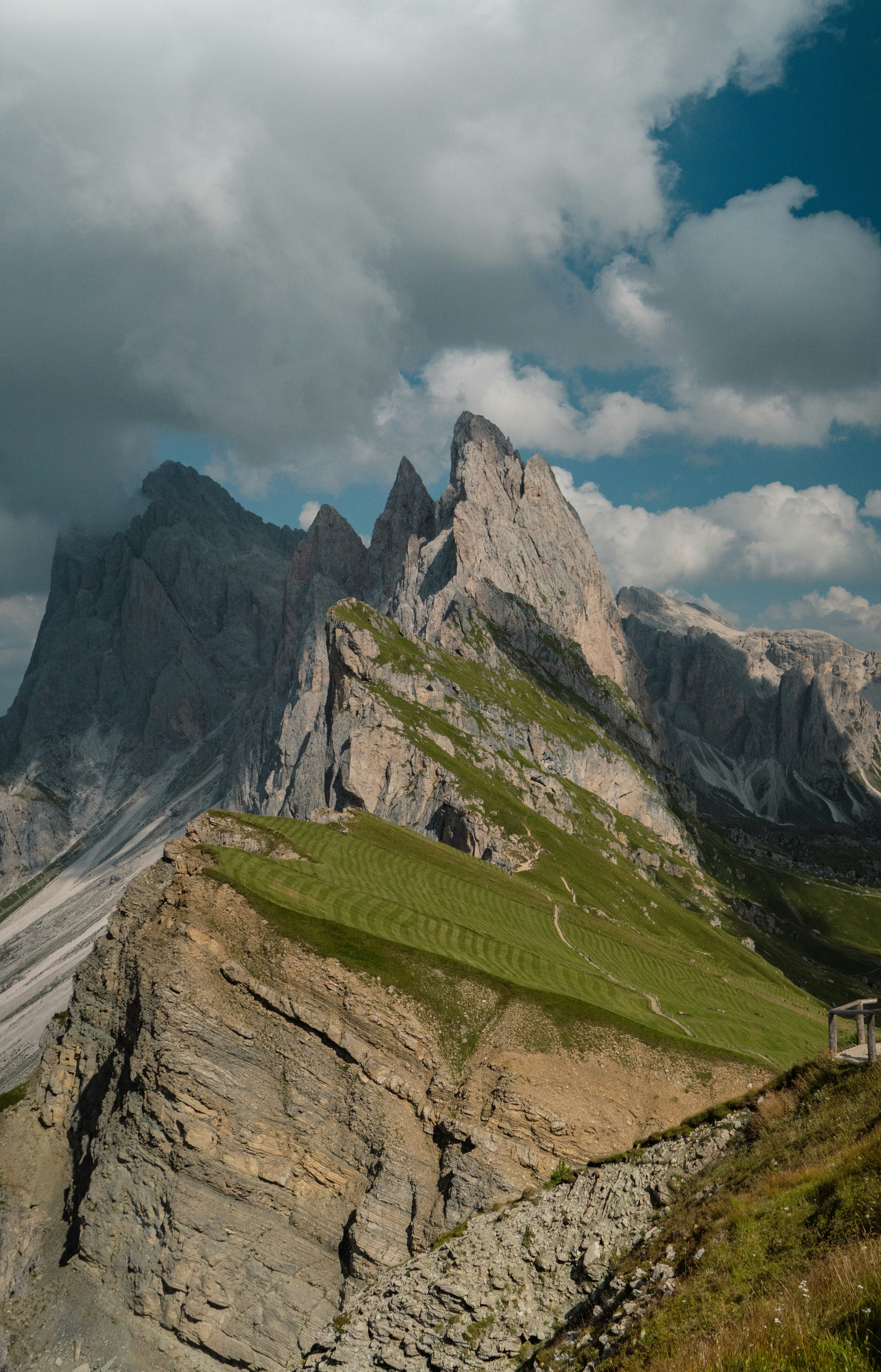 Dramatic mountain peaks rise sharply against a dynamic sky, showcasing the rugged beauty of the Dolomites. Lush green slopes contrast with the rocky terrain, inviting exploration.