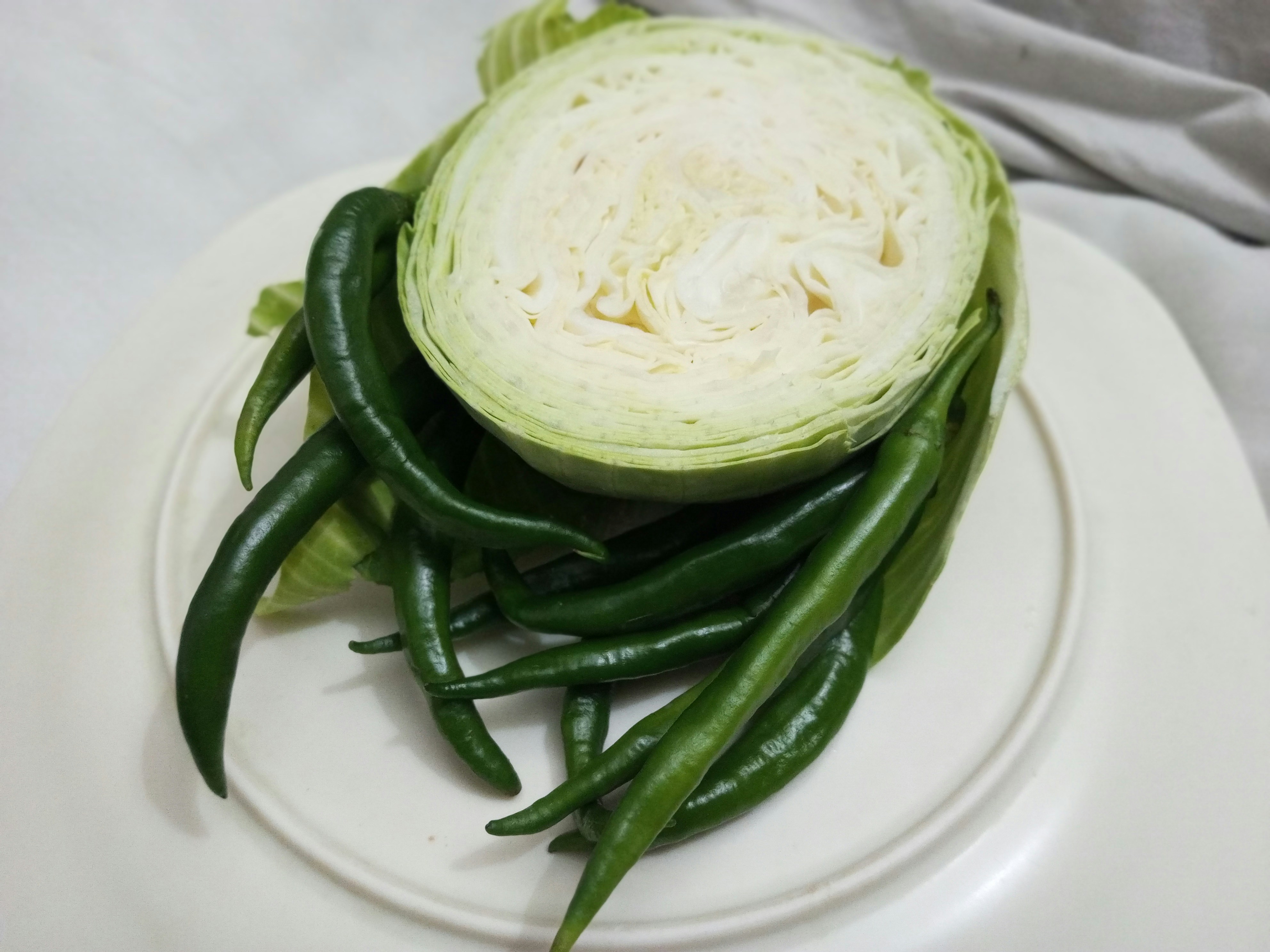 Fresh half cabbage and green chilies. | Half cabbage with green chili peppers on plate