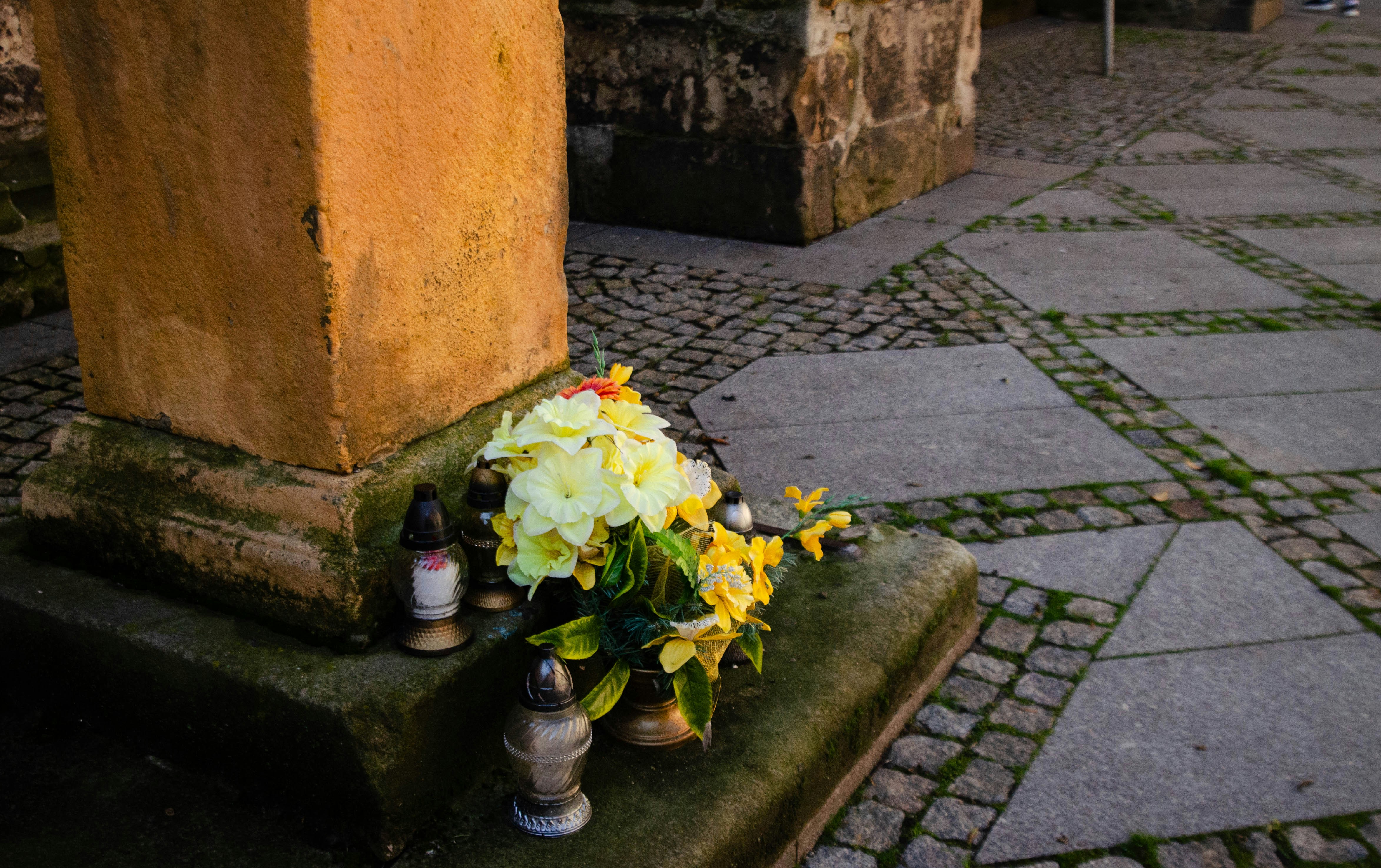 Vibrant artificial flowers and candles arranged at the base of a weathered pillar, symbolizing remembrance and reflection.