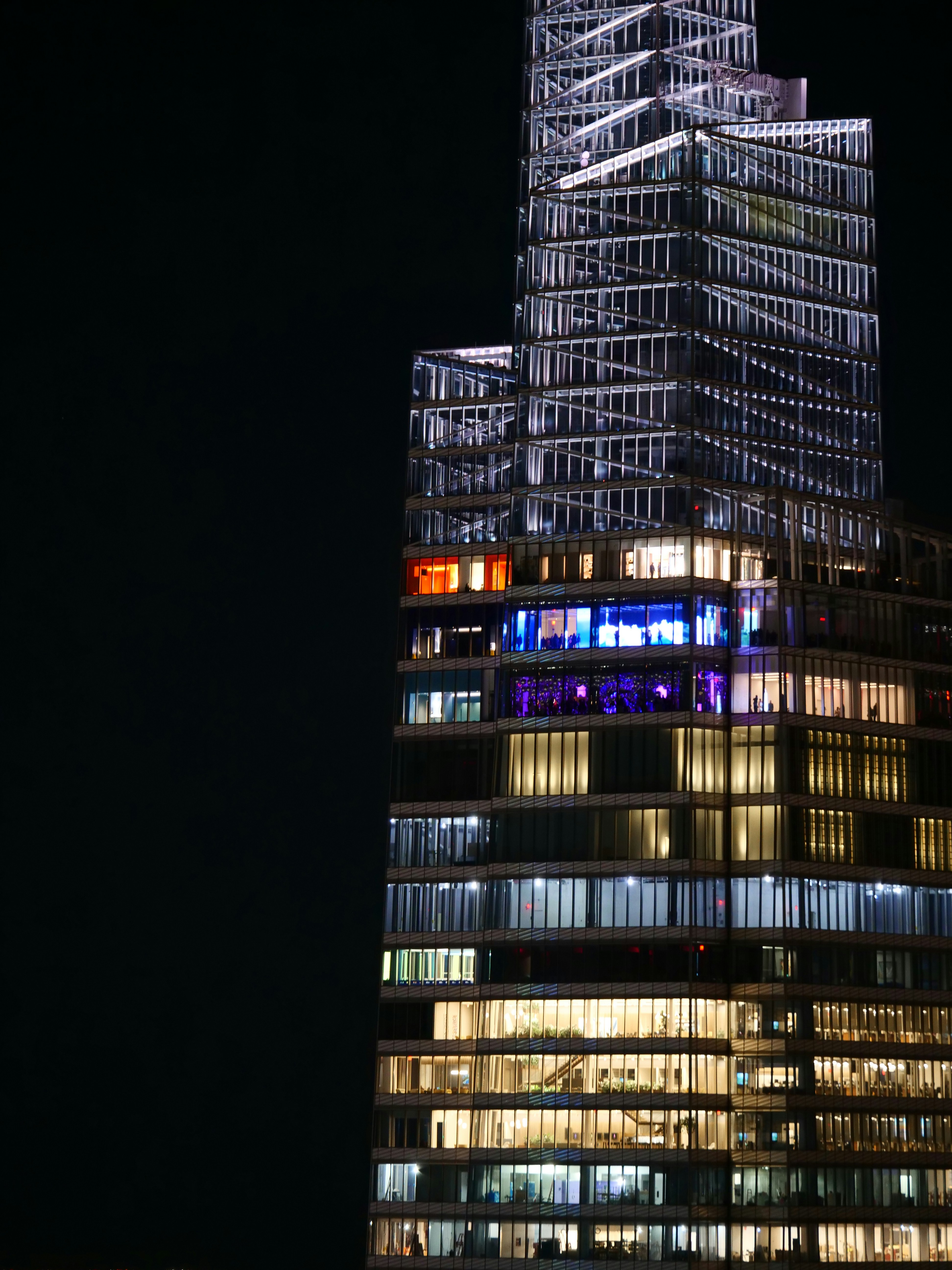 Modern skyscraper illuminated at night with colorful lights.